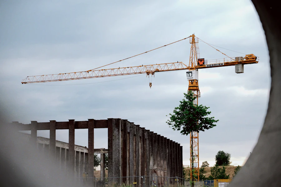 Tower crane poised over industrial site against a cloudy sky, framed by circular concrete structure.