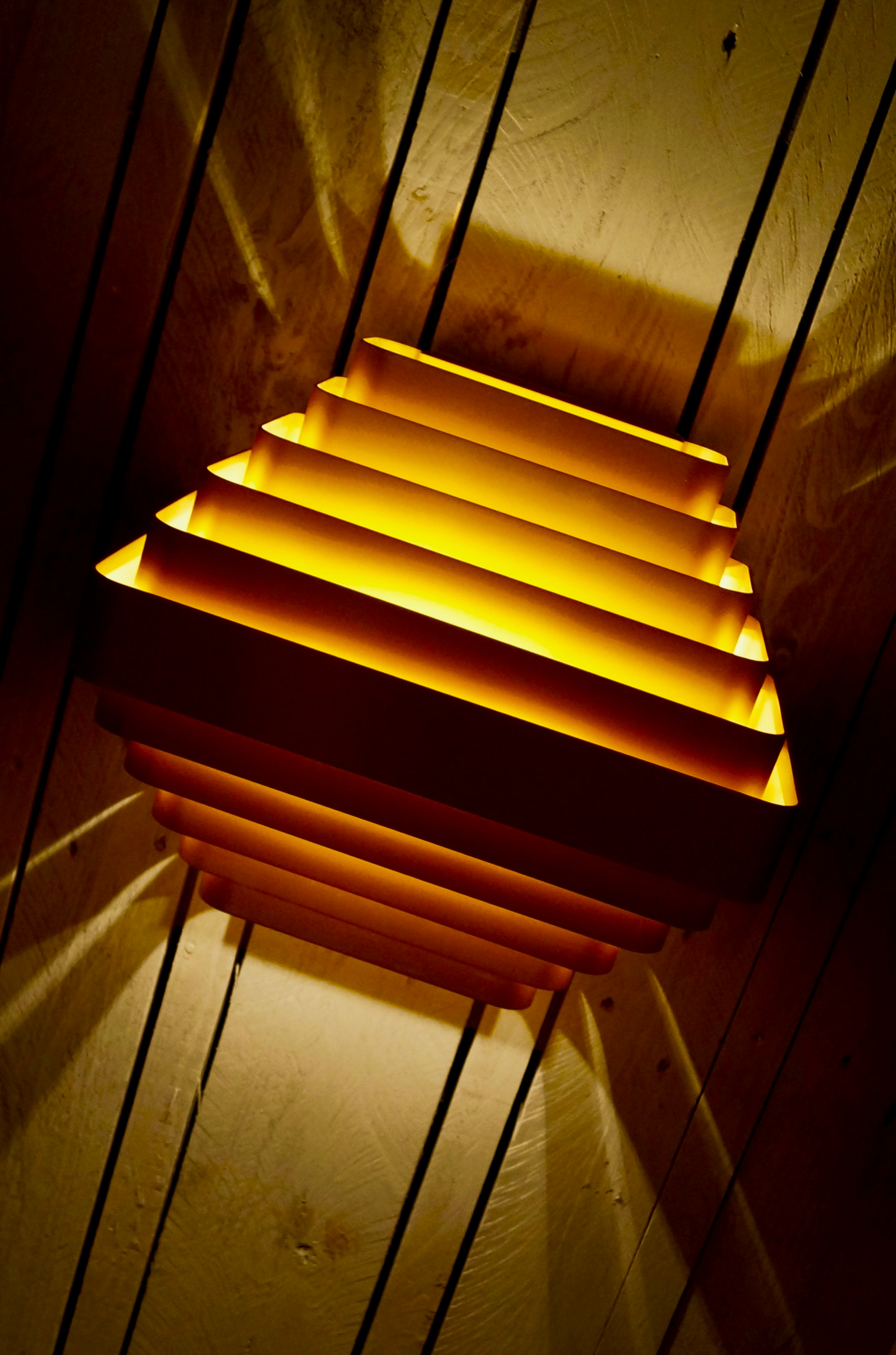 Stylish wooden lamp casting warm light and intricate shadows on a wooden wall.