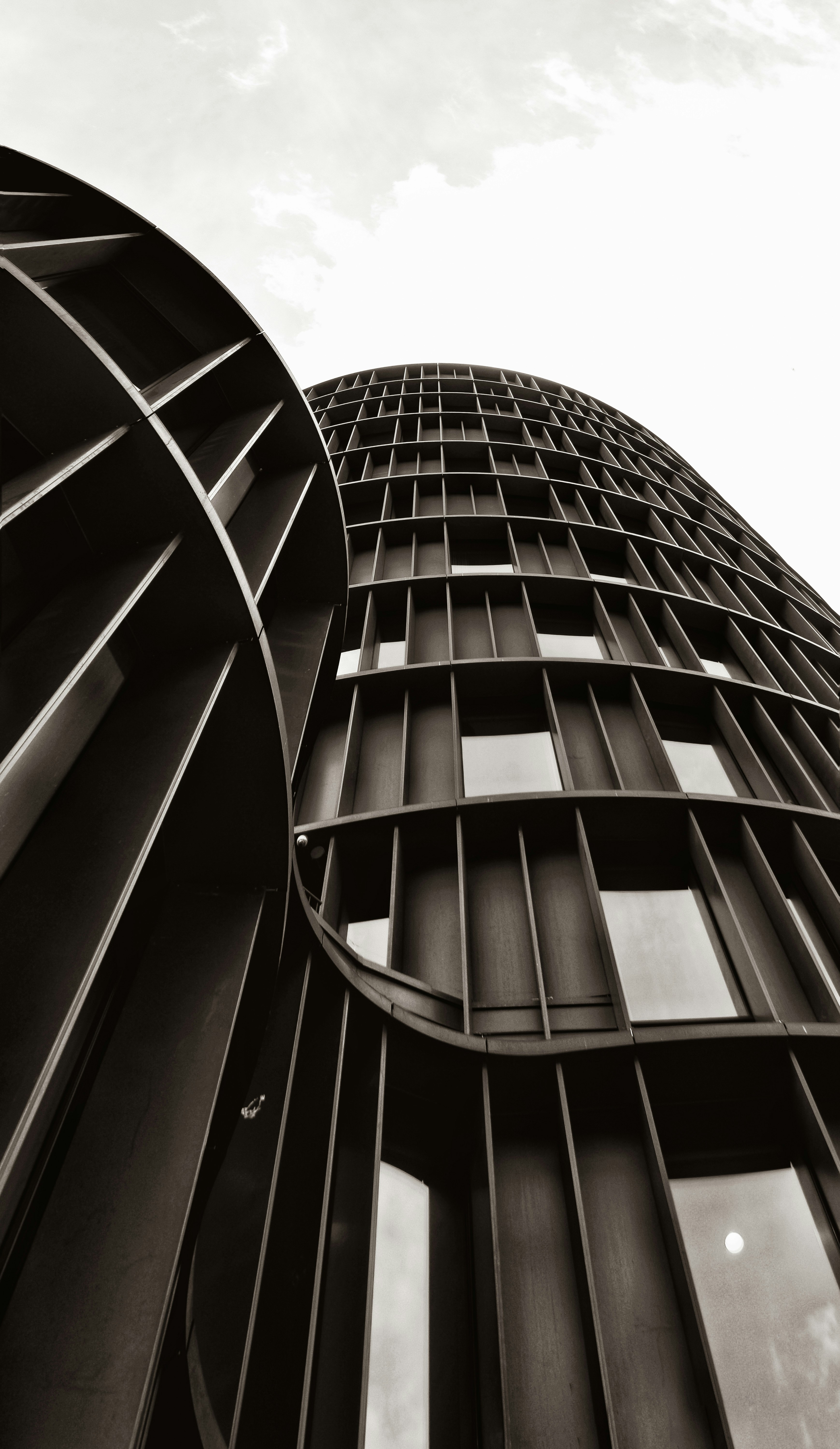 A unique architectural structure showcasing a blend of curved and linear elements, emphasizing modern design. The monochromatic tones highlight the interplay of light and shadow.