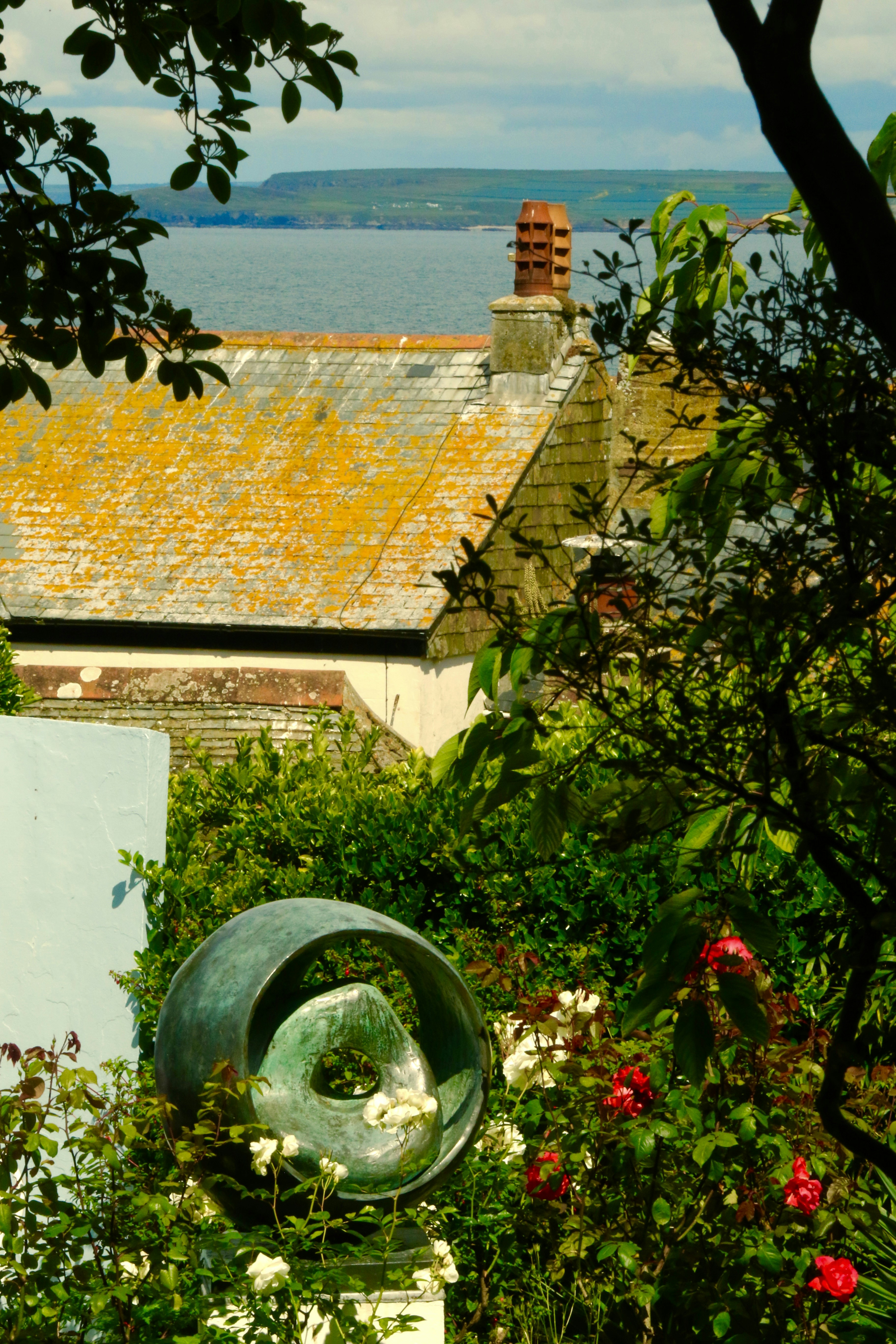 Green Ring in a Sunlit Courtyard: A Weathered Metal Disk Framed by Flowers and a Sea View