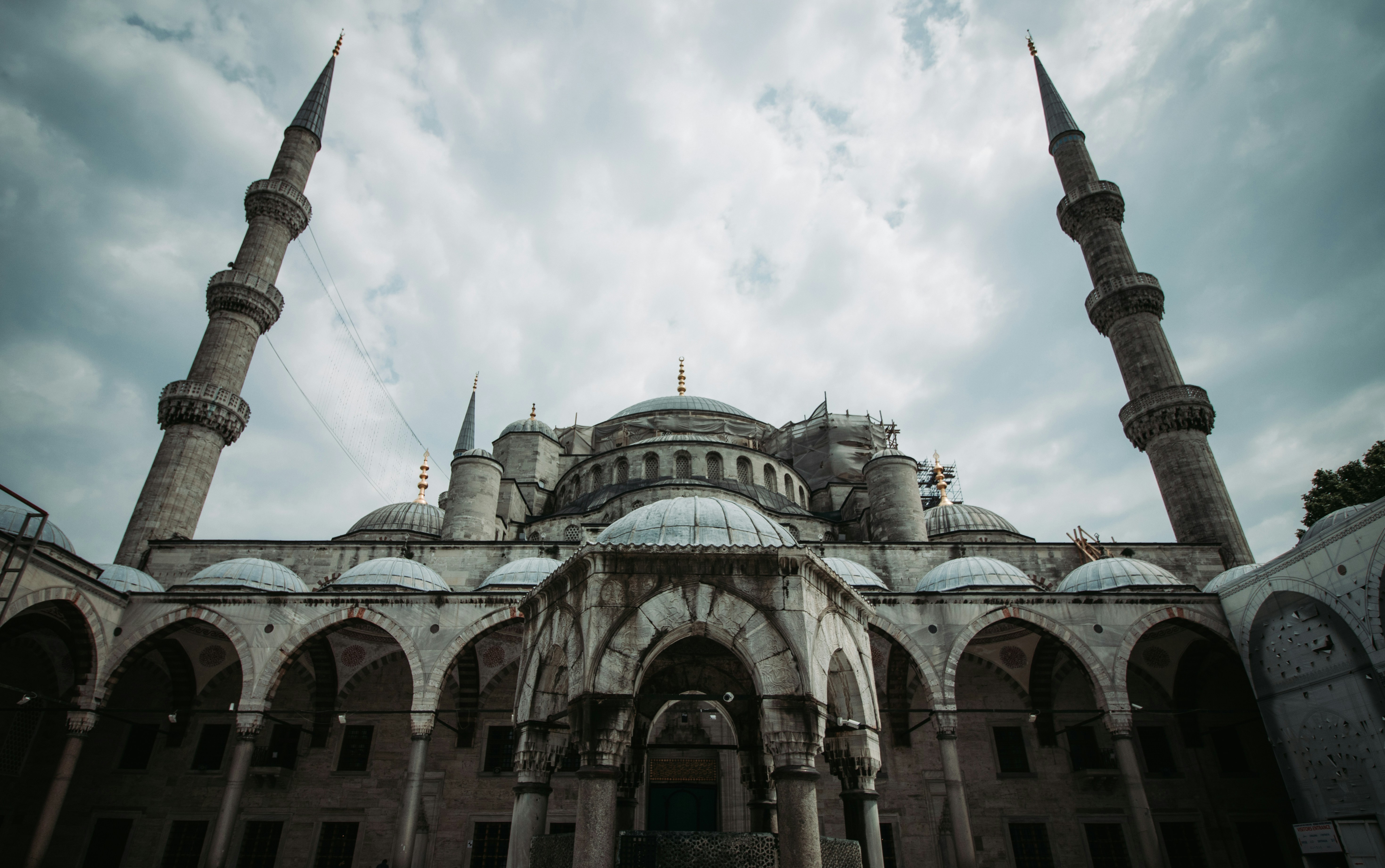 Grand mosque with two towering minarets under a cloudy sky.