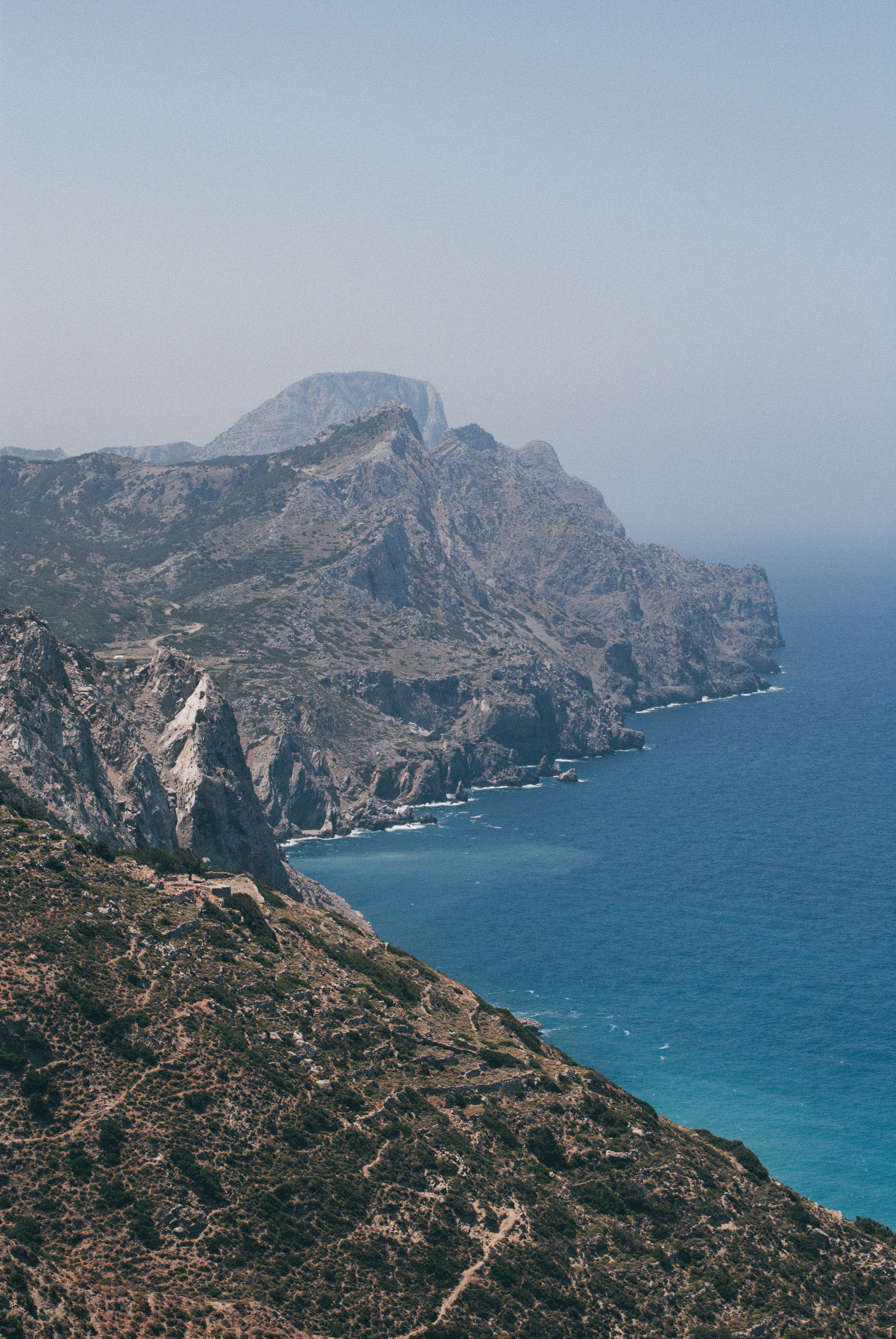 Jagged cliffs extend along a vibrant coastline, meeting the deep blue waters of the sea under a clear sky.