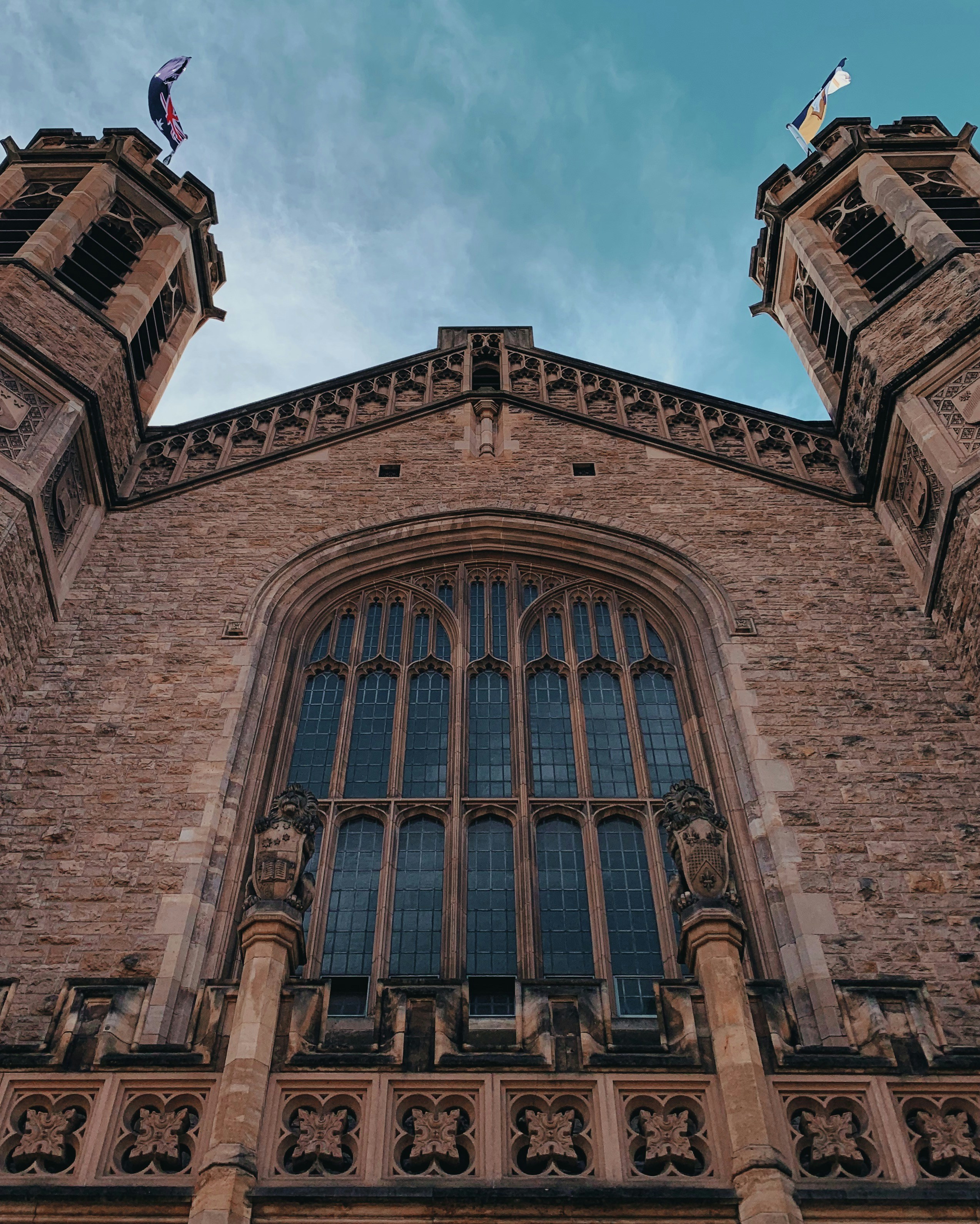 Majestic stone facade of a Gothic-style building with intricate details, viewed from below against a bright sky.