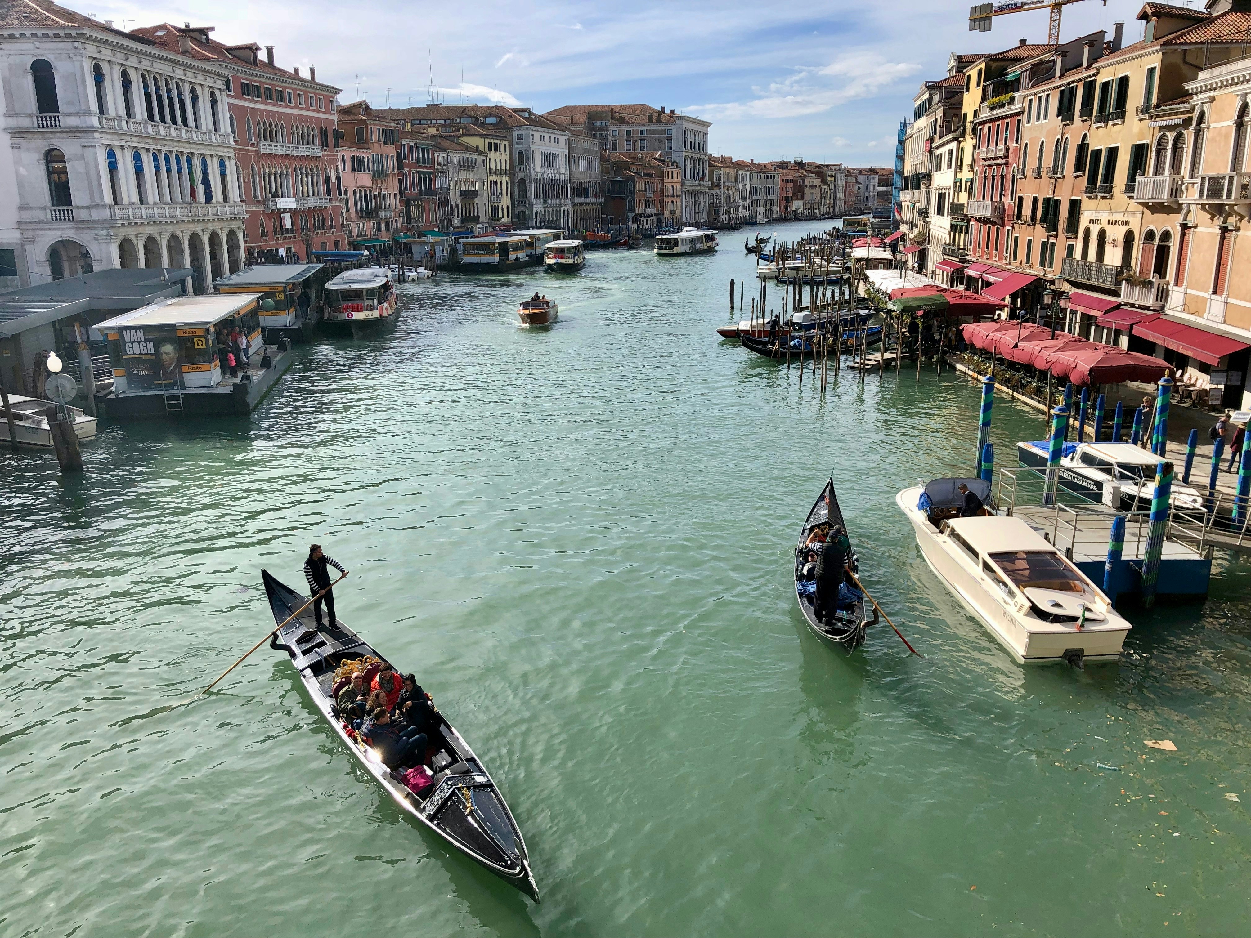 Gondolas glide through a canal in Venice, flanked by historic buildings and a bustling waterfront.