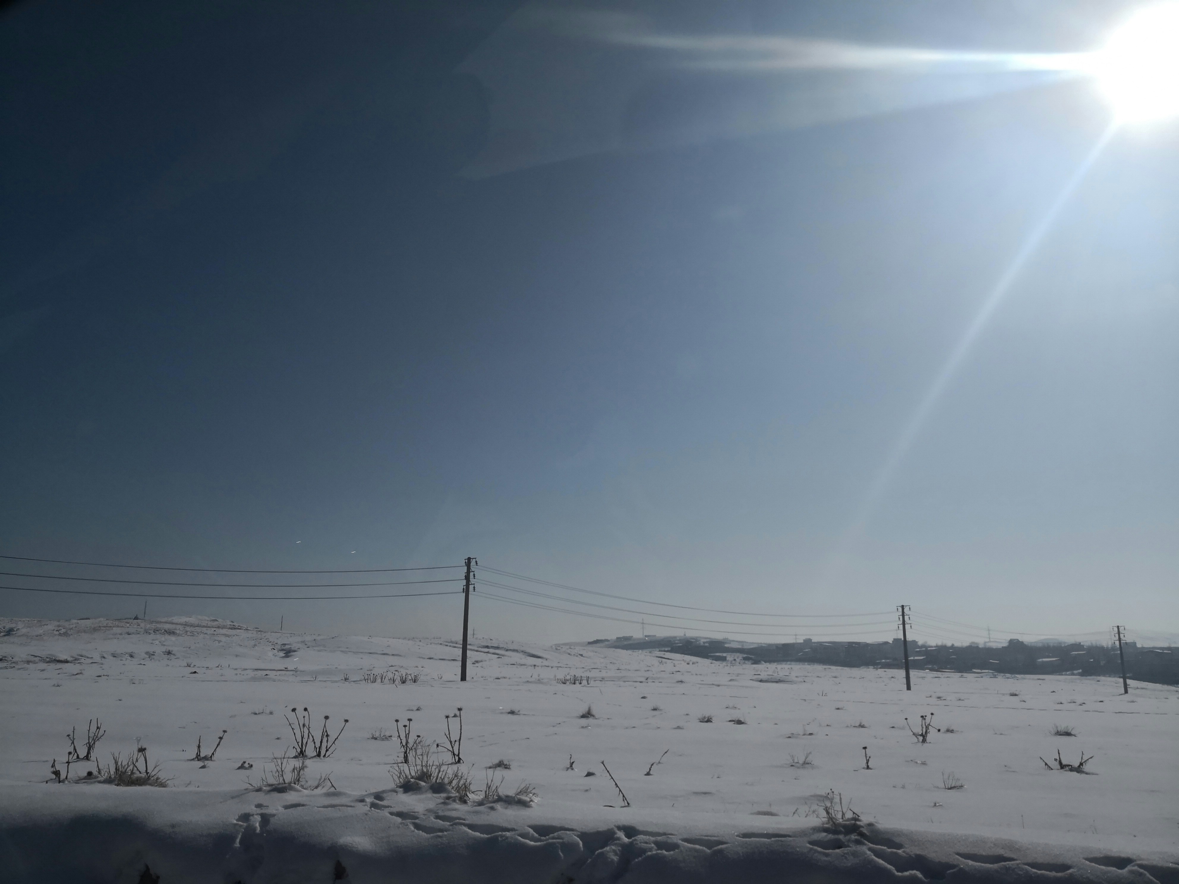 Expansive snowy landscape under a clear blue sky, with distant power lines cutting through the serene scene.