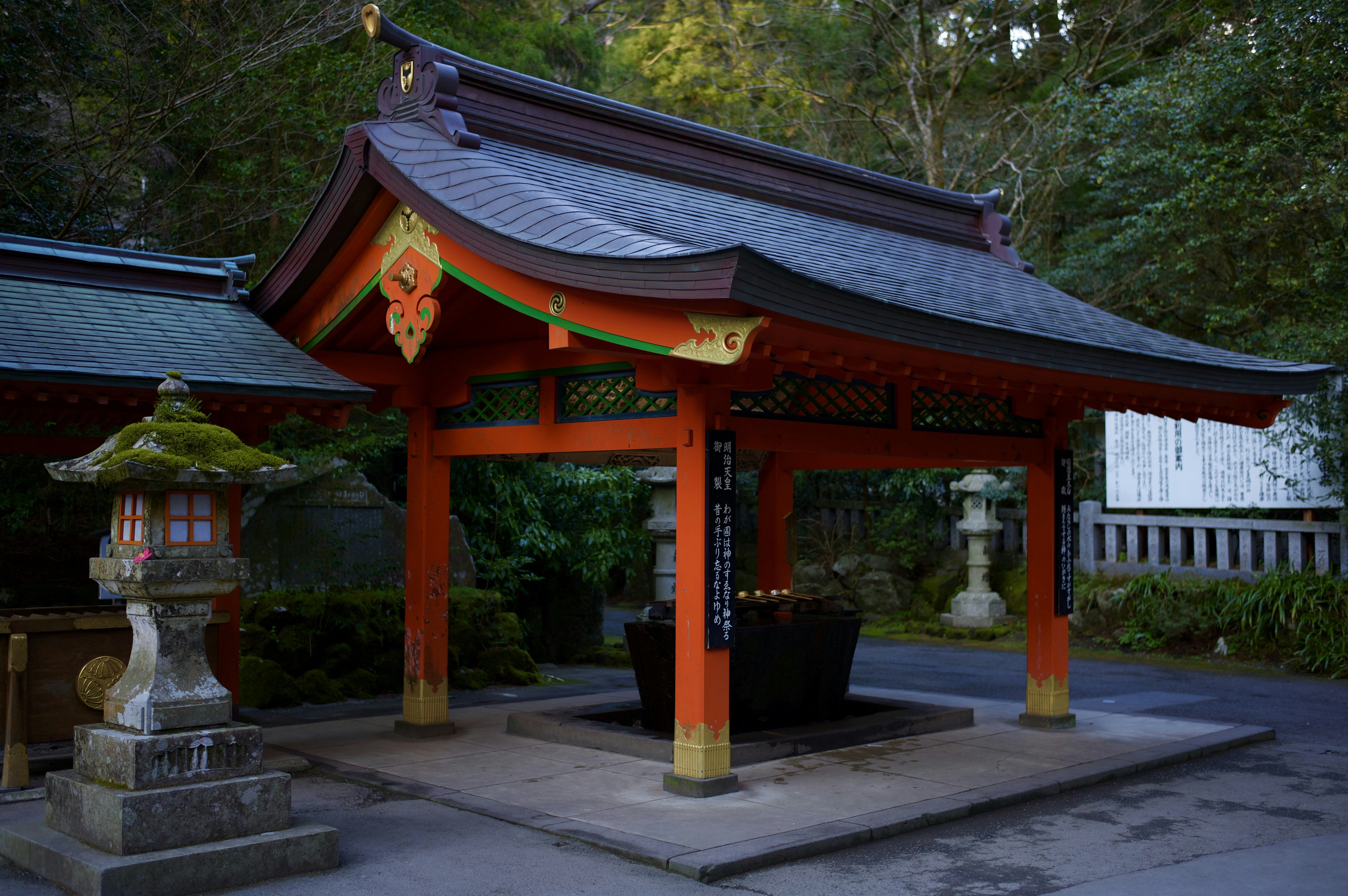 Traditional Japanese shrine with vibrant red architecture and stone lanterns surrounded by lush greenery. The serene atmosphere invites reflection.