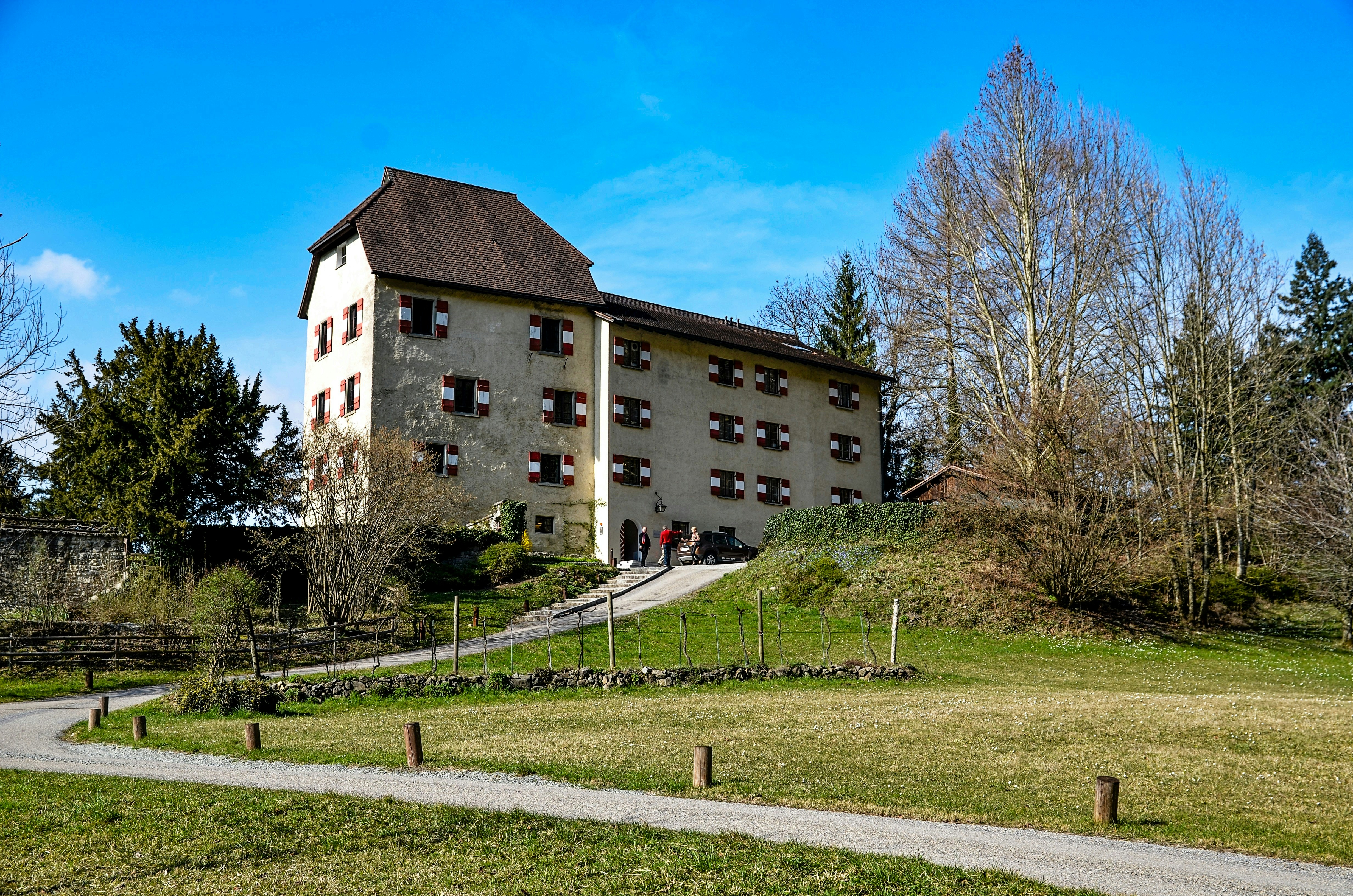 Stone building with a steep roof surrounded by bare winter trees under a clear blue sky.