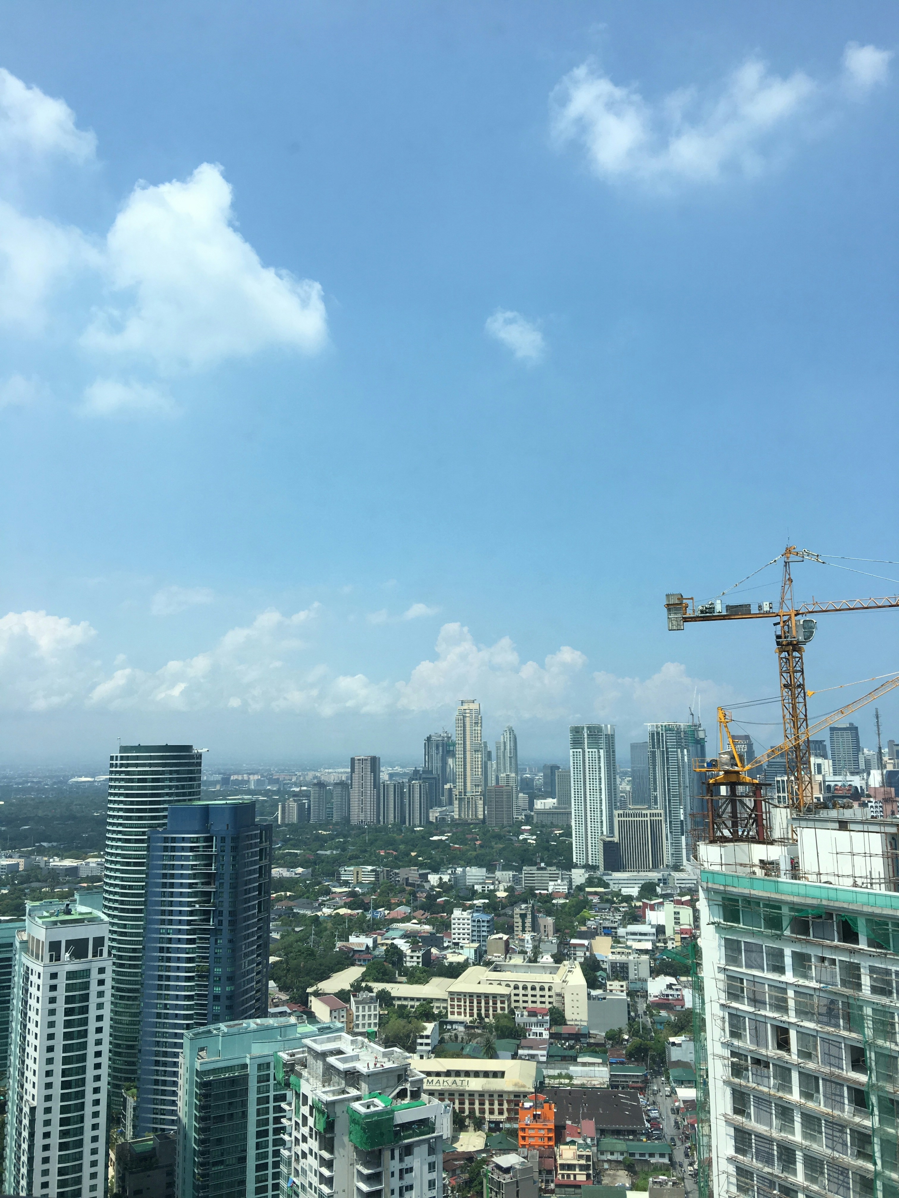 A panoramic view of a bustling city skyline featuring a mix of modern skyscrapers and low-rise buildings under a vibrant blue sky. The scene captures the dynamic essence of urban life.