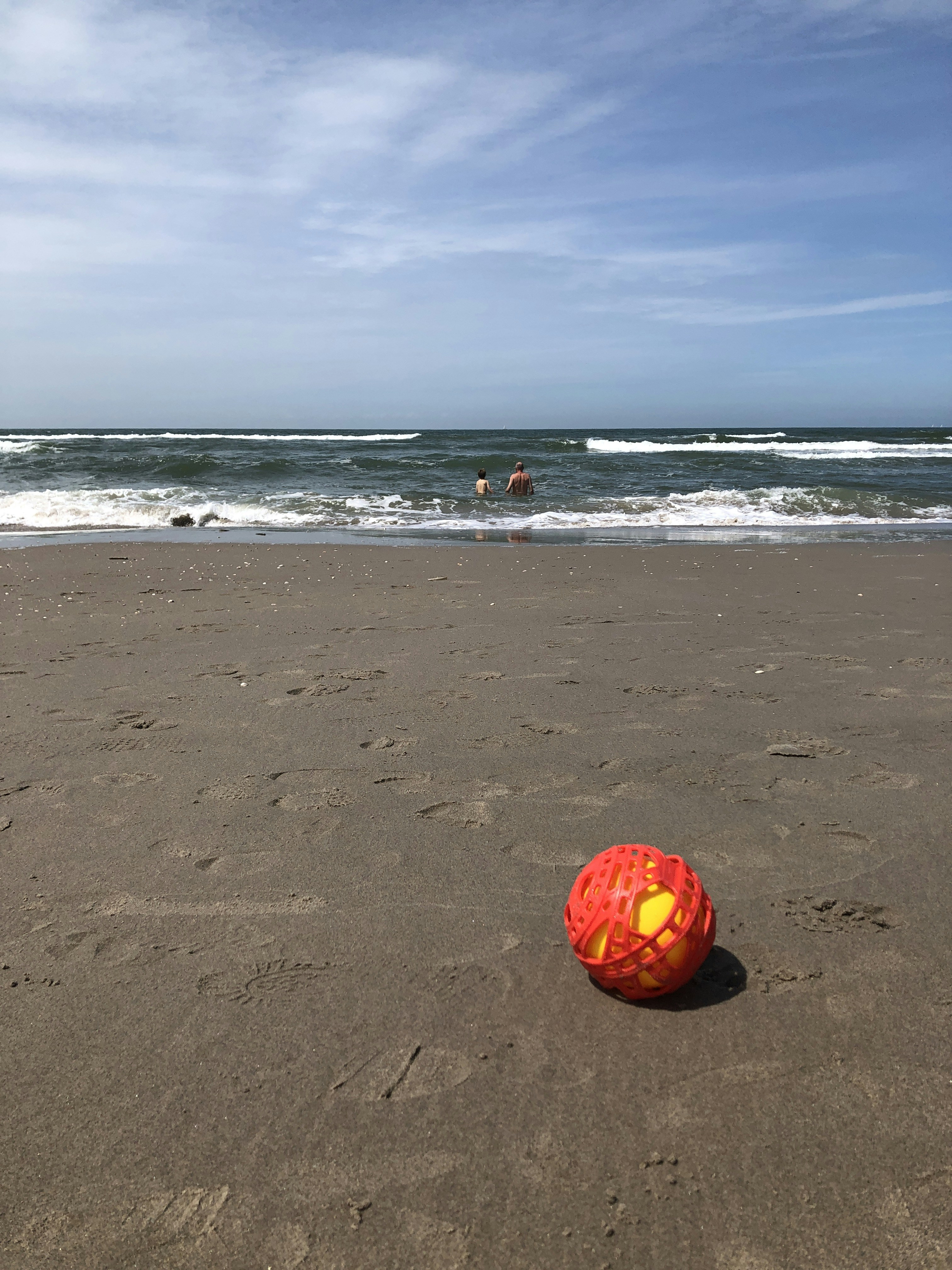 Crimson Ball on the Quiet Shore: Footprints, Foam, and Distant Figures