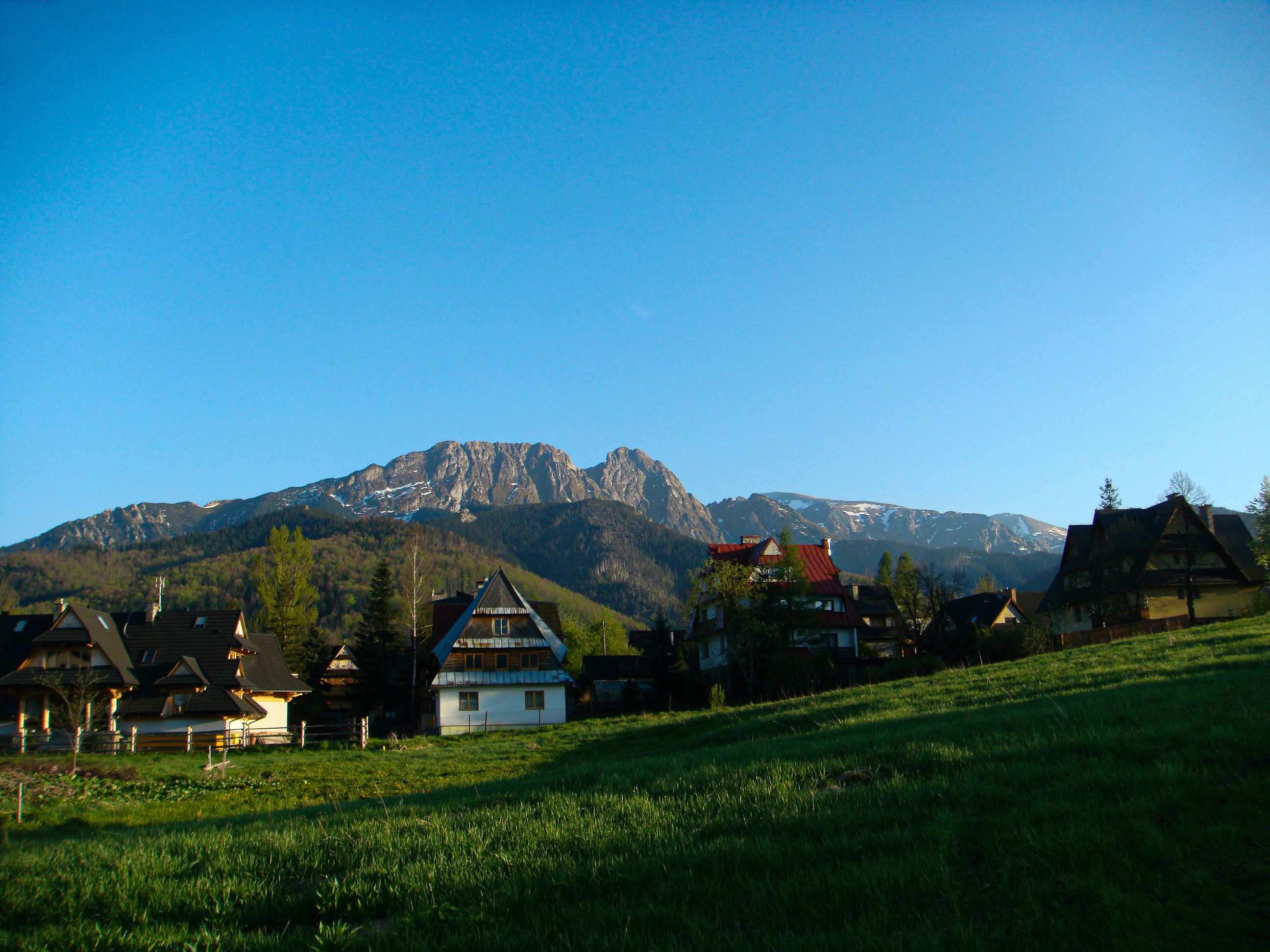 Charming village houses nestled against a backdrop of majestic mountains under a clear blue sky.