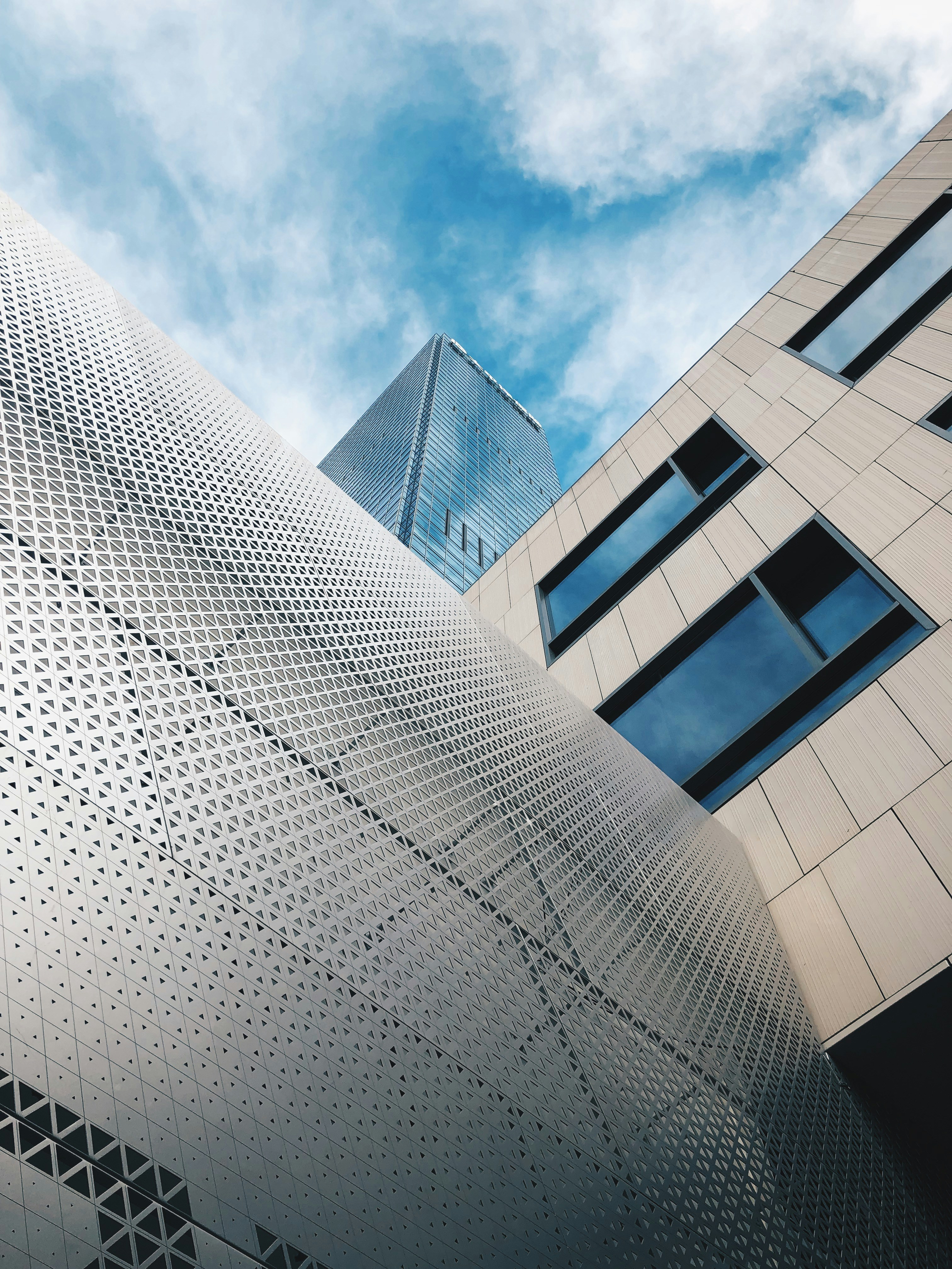 Geometric patterns of a metallic façade reflect a towering skyscraper against a vibrant sky. The interplay of light and structure highlights contemporary architectural design.