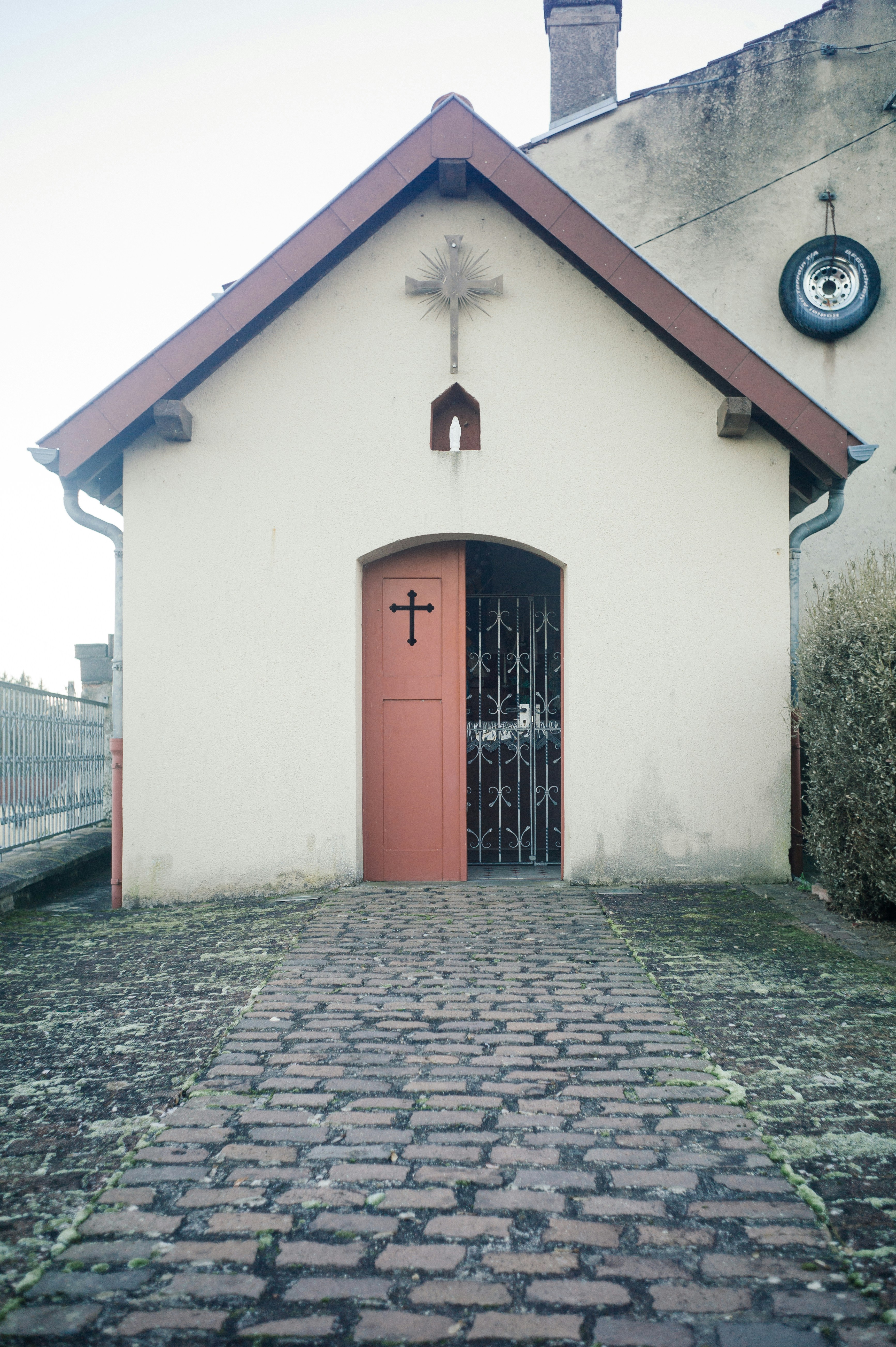 A quaint chapel with a pink door and cross, framed by a cobblestone path leading to its entrance. The simplicity of its design evokes a sense of peace.