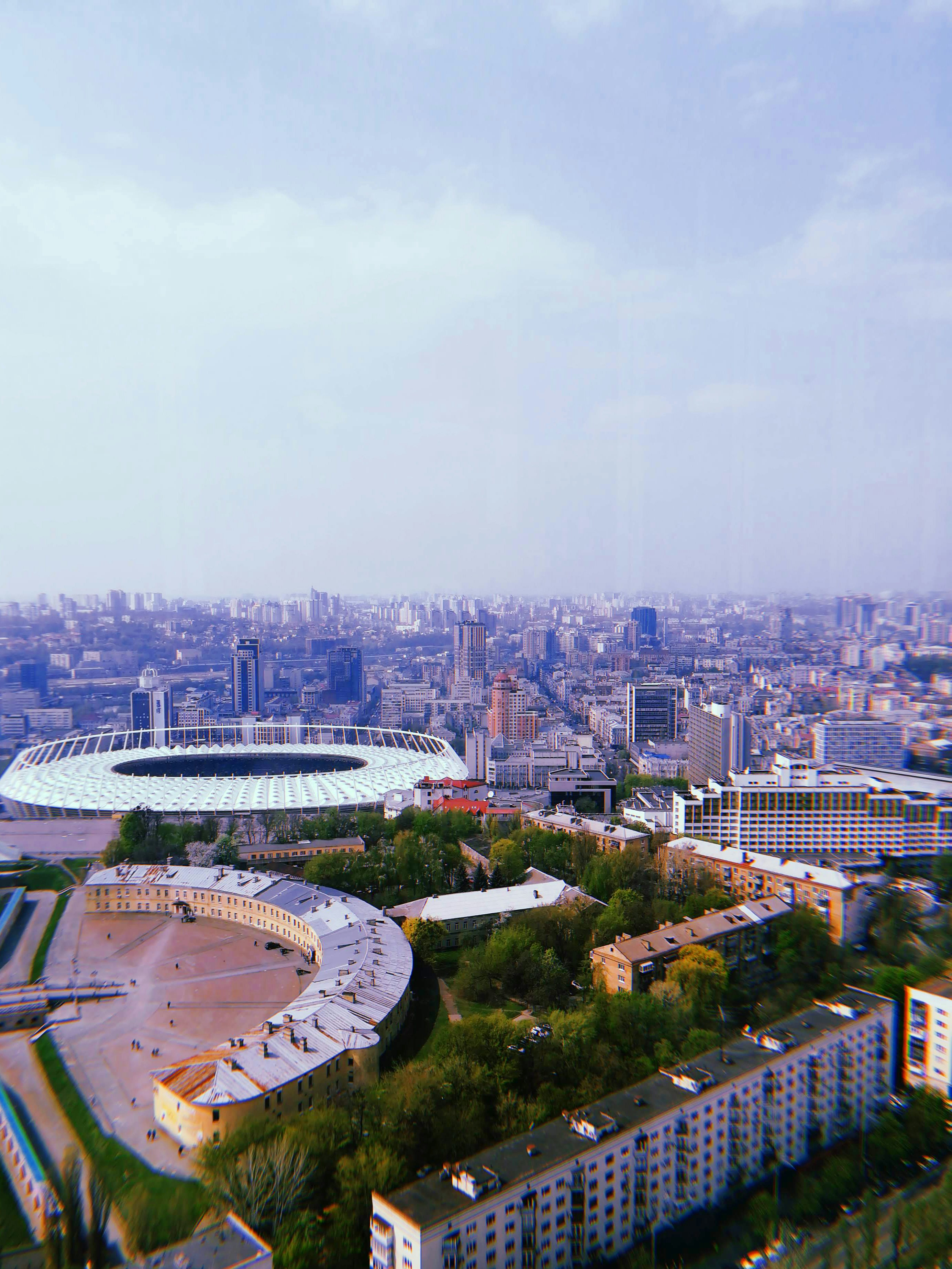 Aerial view of a vibrant cityscape featuring a modern stadium, lush parks, and residential buildings, showcasing the blend of architecture and nature.