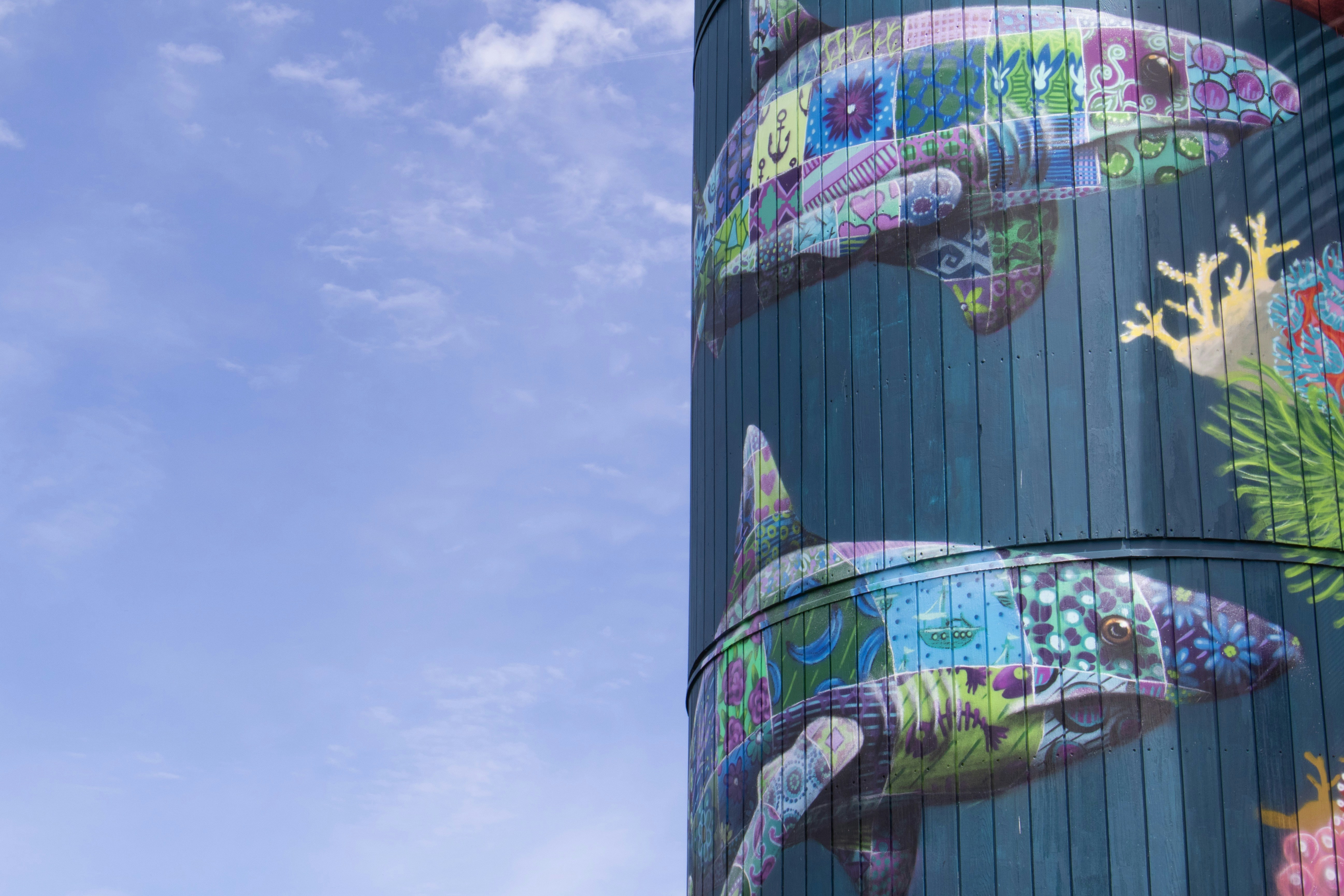 Colorful mural of whales and coral on a cylindrical building under a bright blue sky.