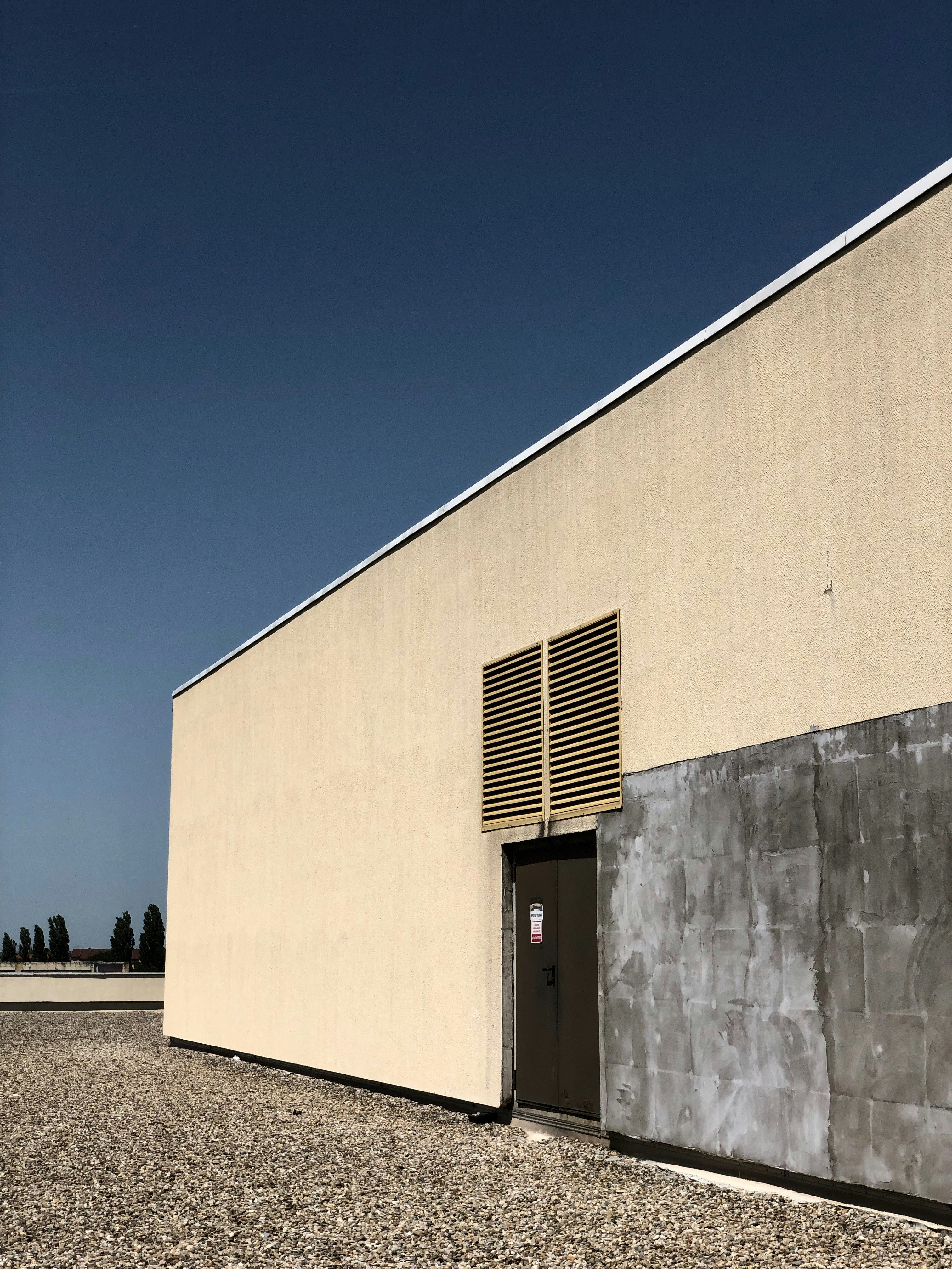 A modern building facade featuring a textured wall and slatted vents against a clear blue sky.
