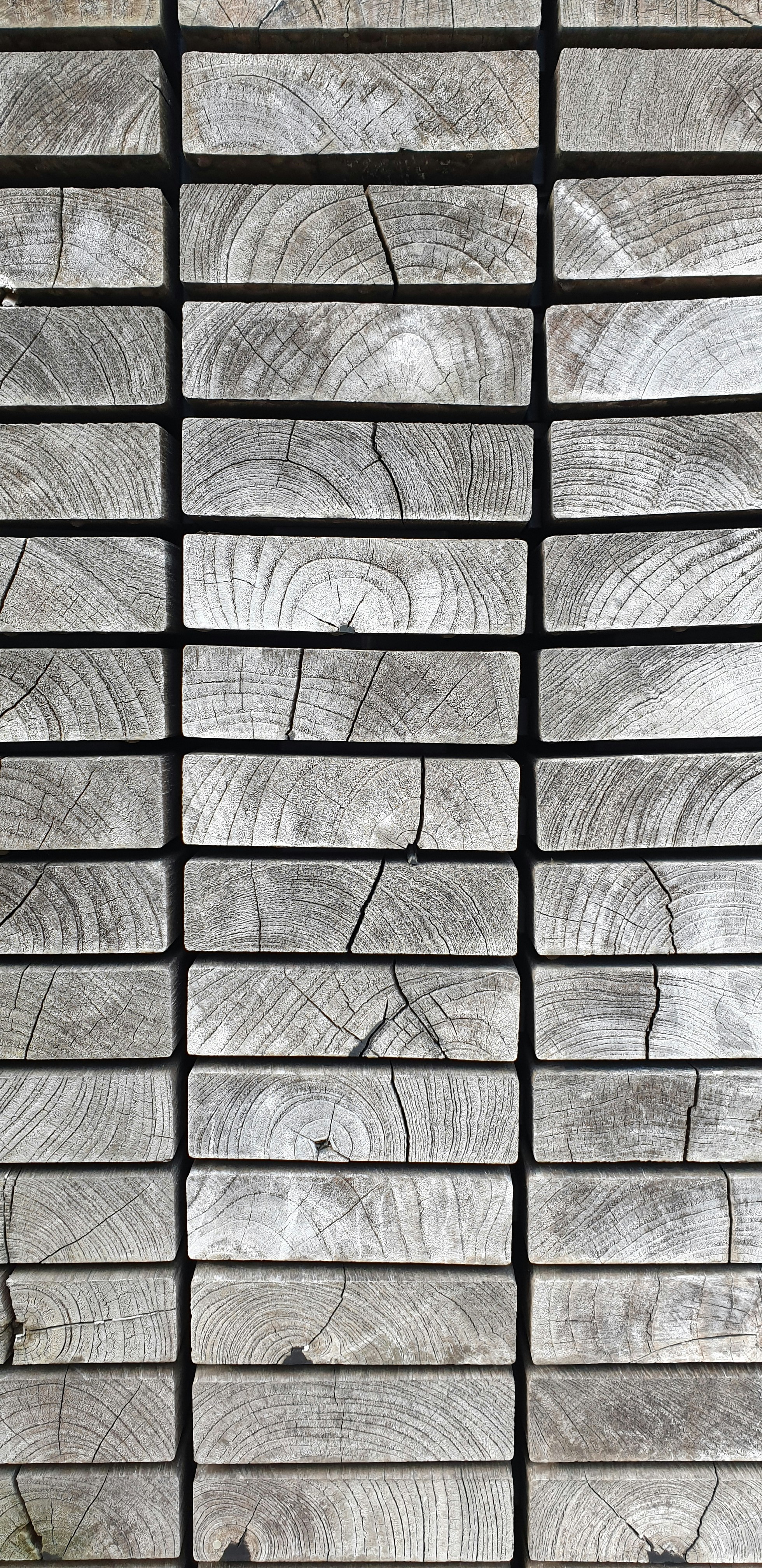 Close-up view of stacked wooden planks showcasing intricate grain patterns and natural cracks. The arrangement highlights the beauty of raw timber.
