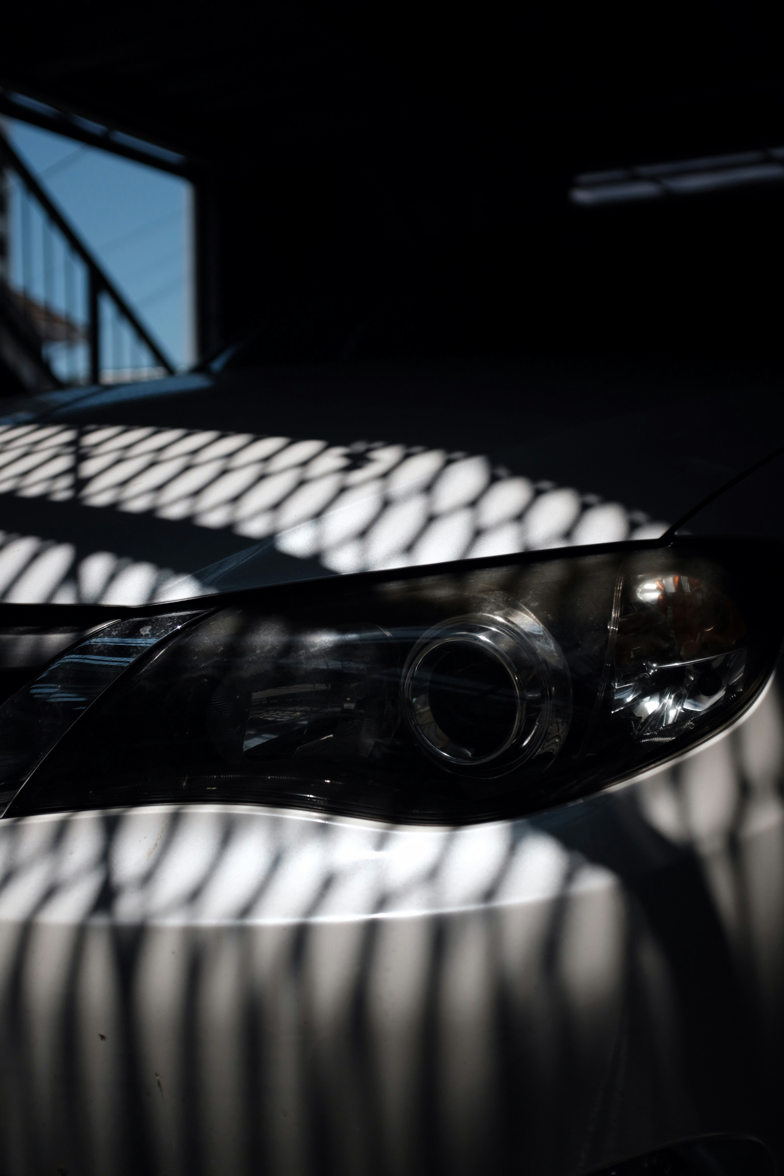 Crisscross Shadows Graze a Car Headlight