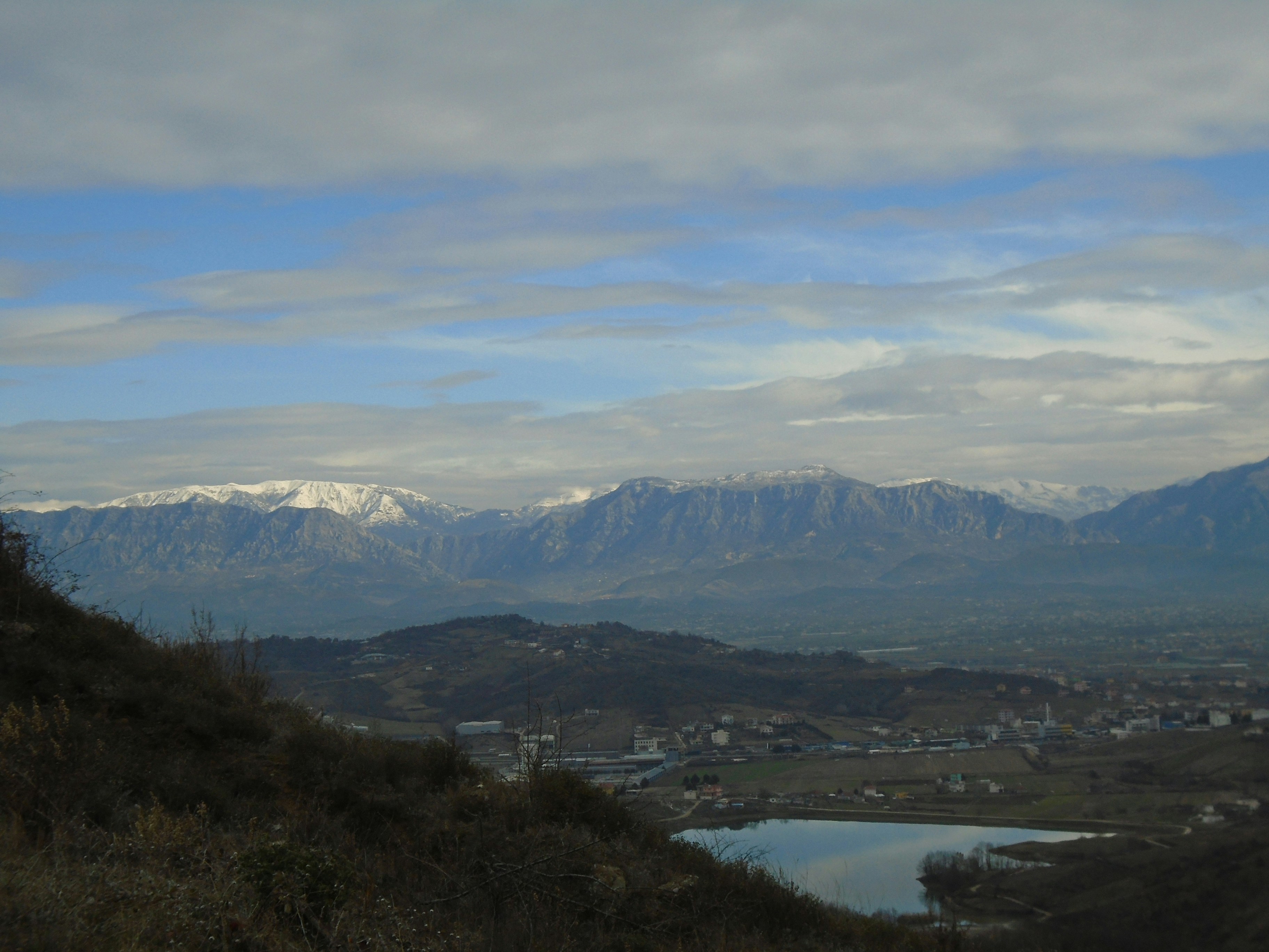 Snow-capped mountains loom over a serene landscape, reflecting in a tranquil body of water below. The scene captures the harmony between nature and the sky.