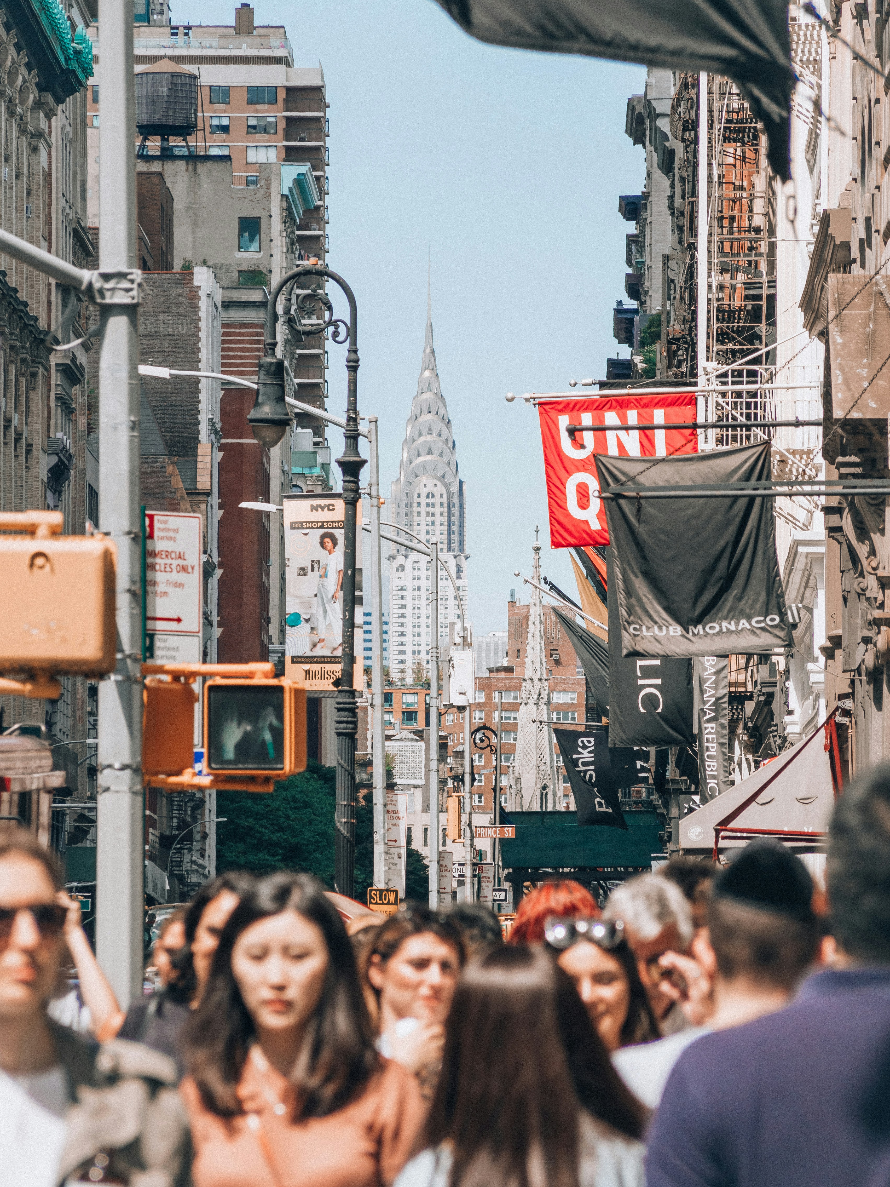 Bustling street scene in New York City with the Chrysler Building framed between tall buildings and vibrant banners.