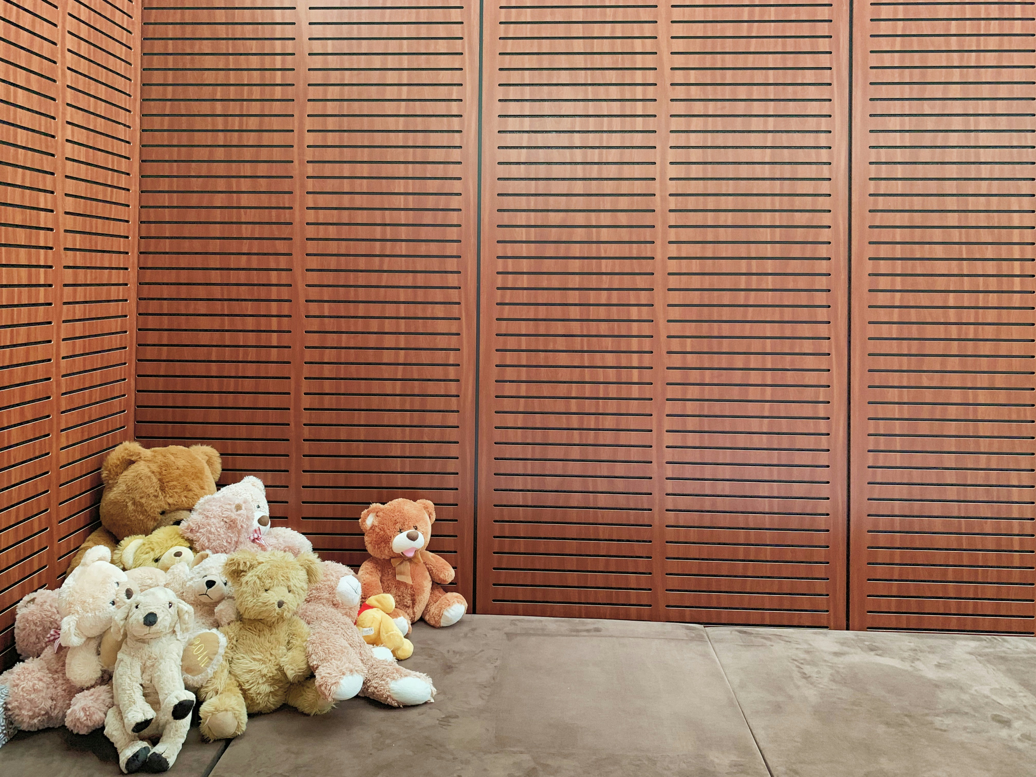 Pile of plush teddy bears nestled against a wooden slatted wall.