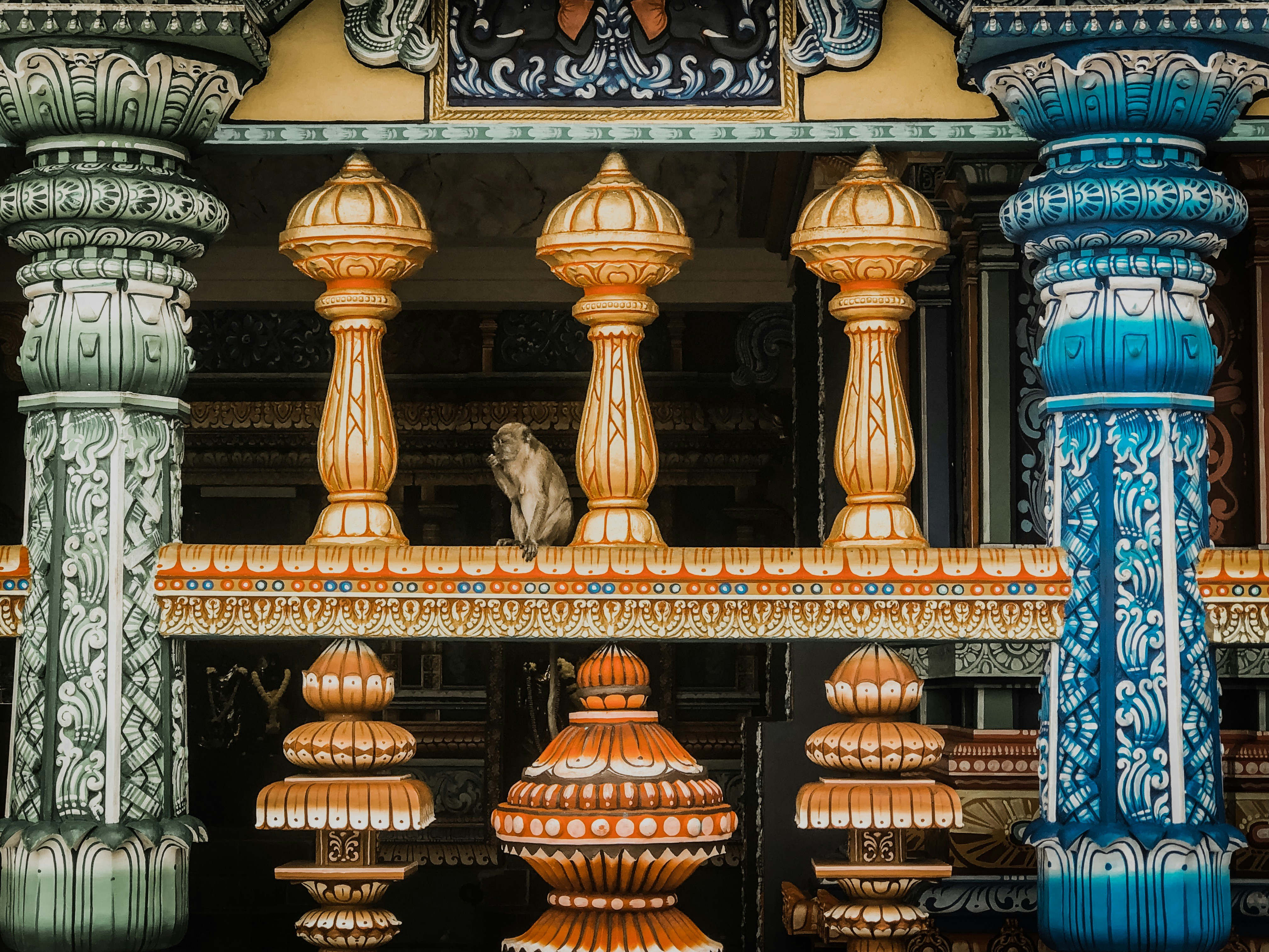 Monkey perched among intricately decorated multicolored pillars.