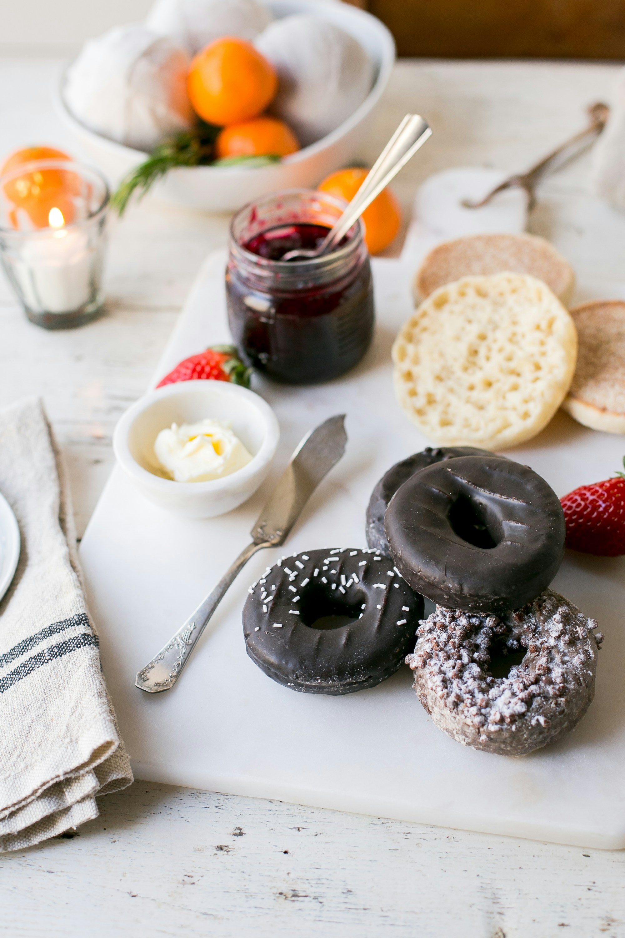 A delightful arrangement featuring assorted donuts, fresh strawberries, and a jar of jam alongside a bowl of oranges. Perfect for a cozy brunch setting.