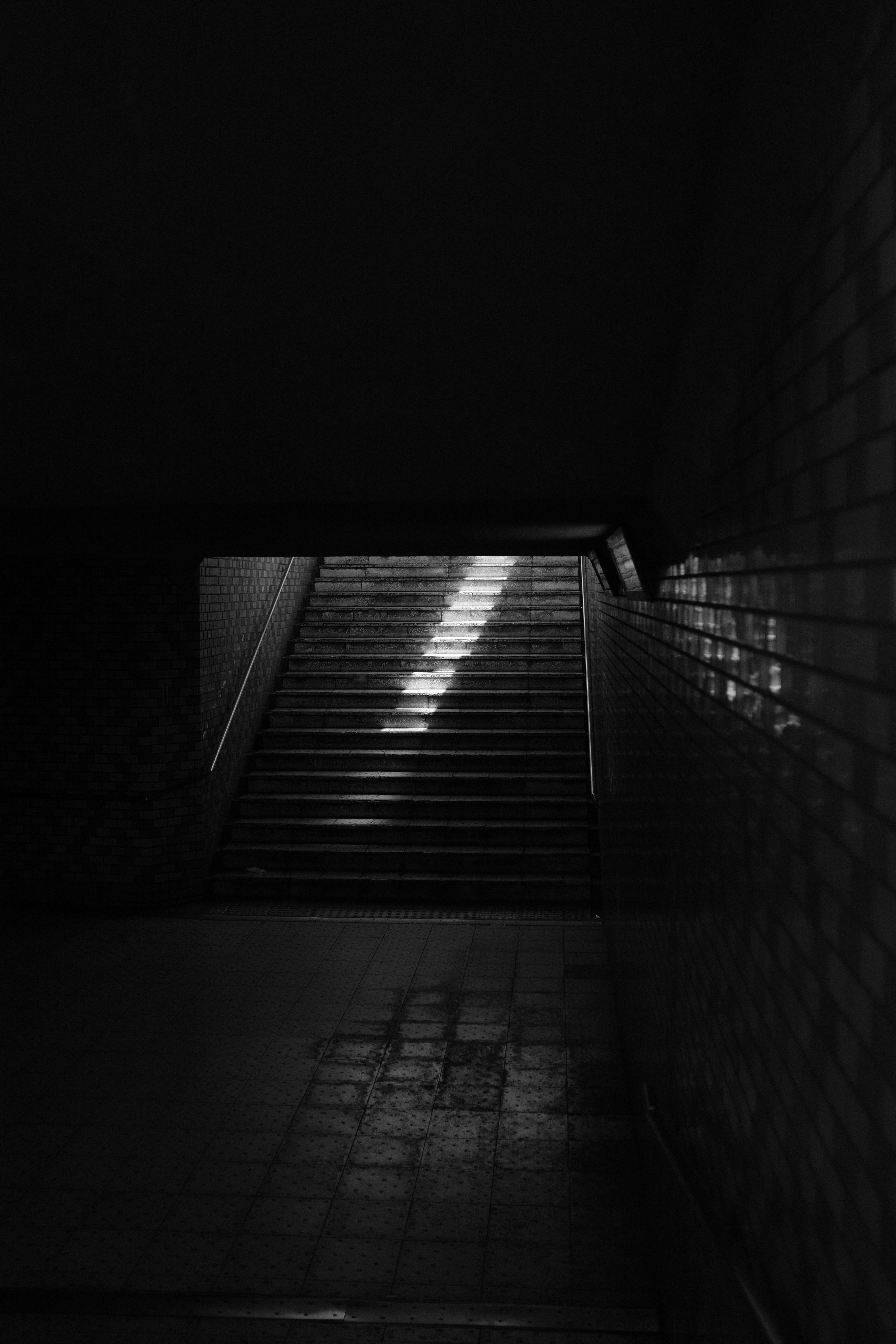 A dimly lit staircase illuminated by a narrow beam of light, creating a striking contrast between light and shadow.