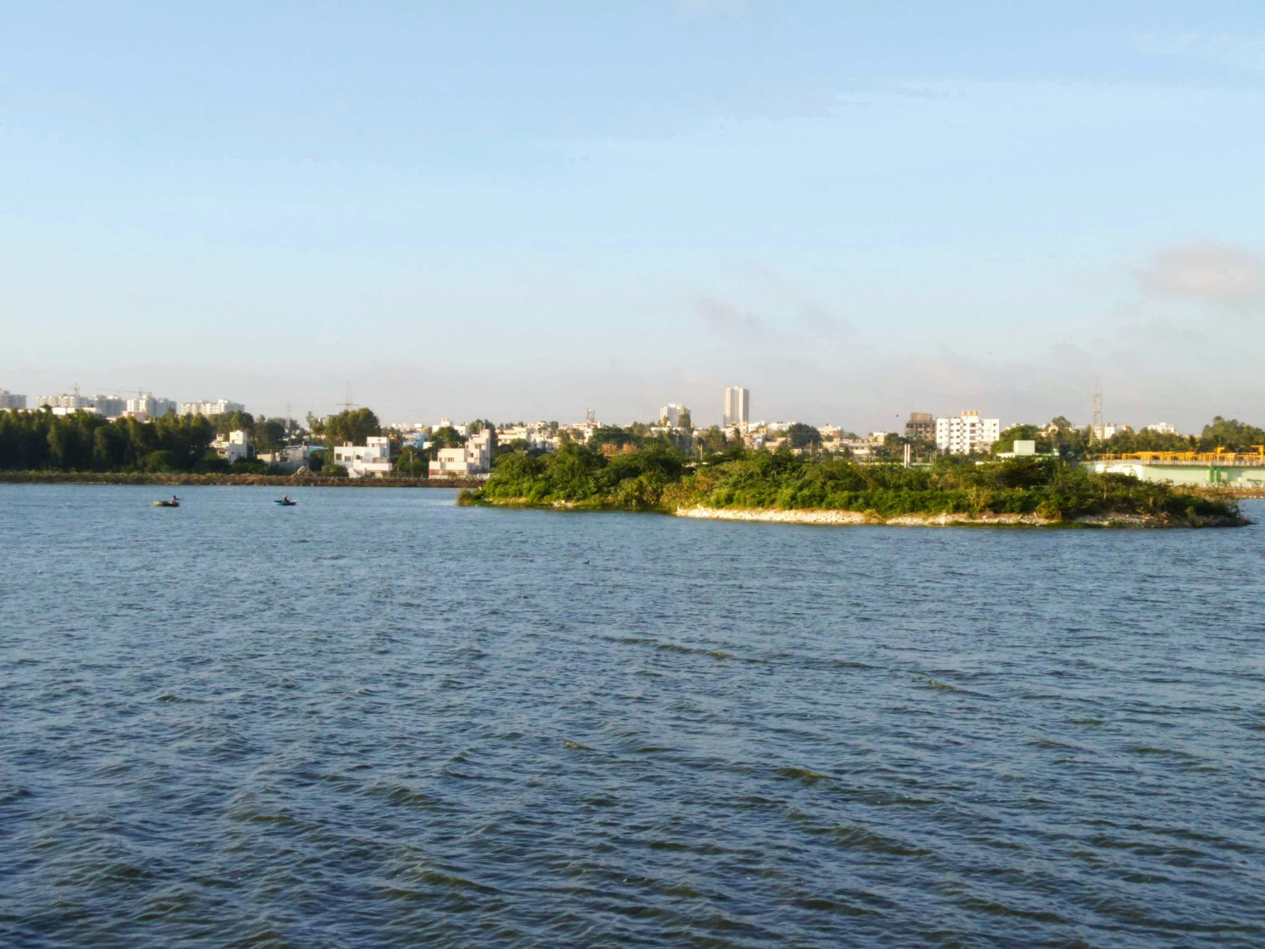 Calm lake with a distant view of a cityscape under a clear blue sky.