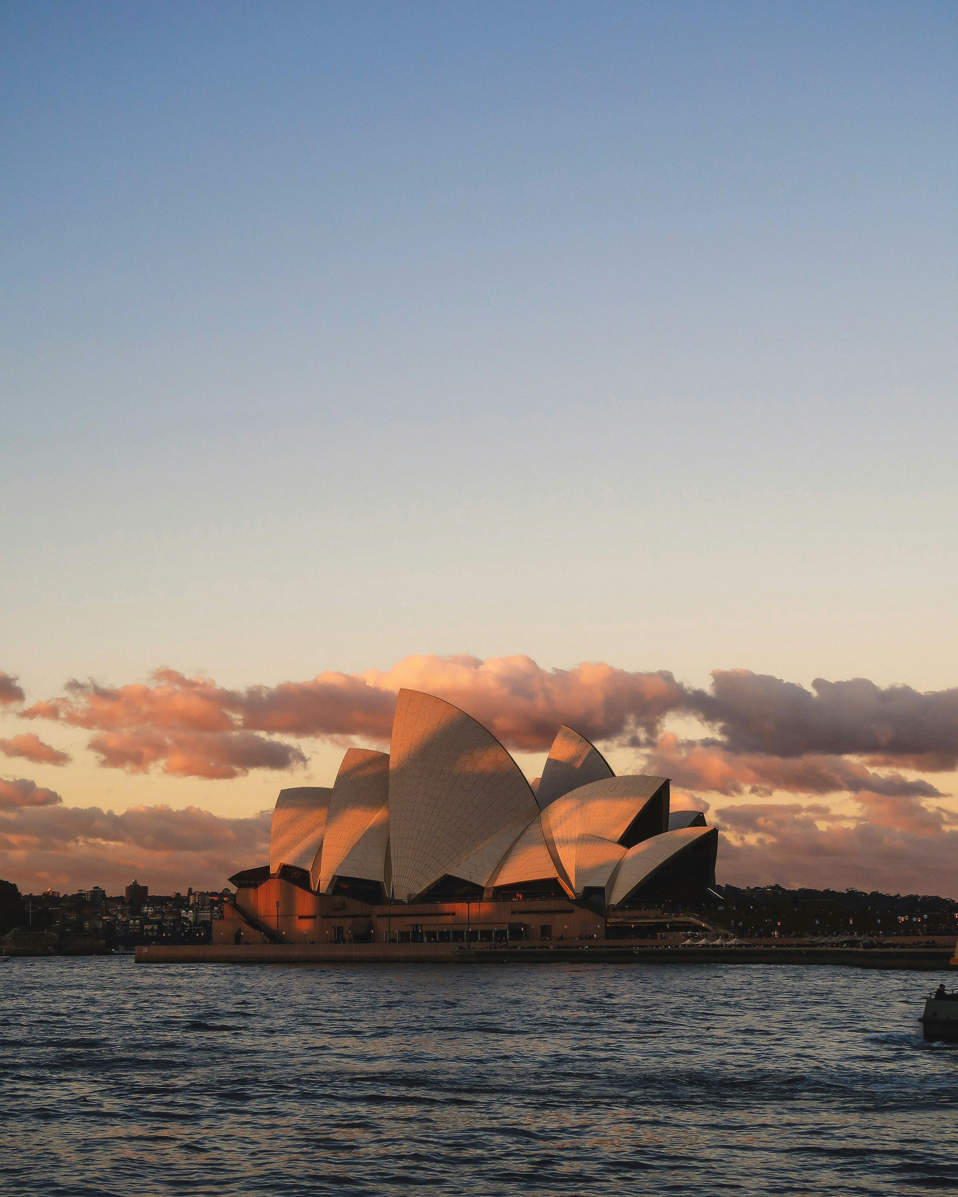 The iconic Sydney Opera House glows under a twilight sky, reflecting the warm hues of sunset on its unique architectural forms.