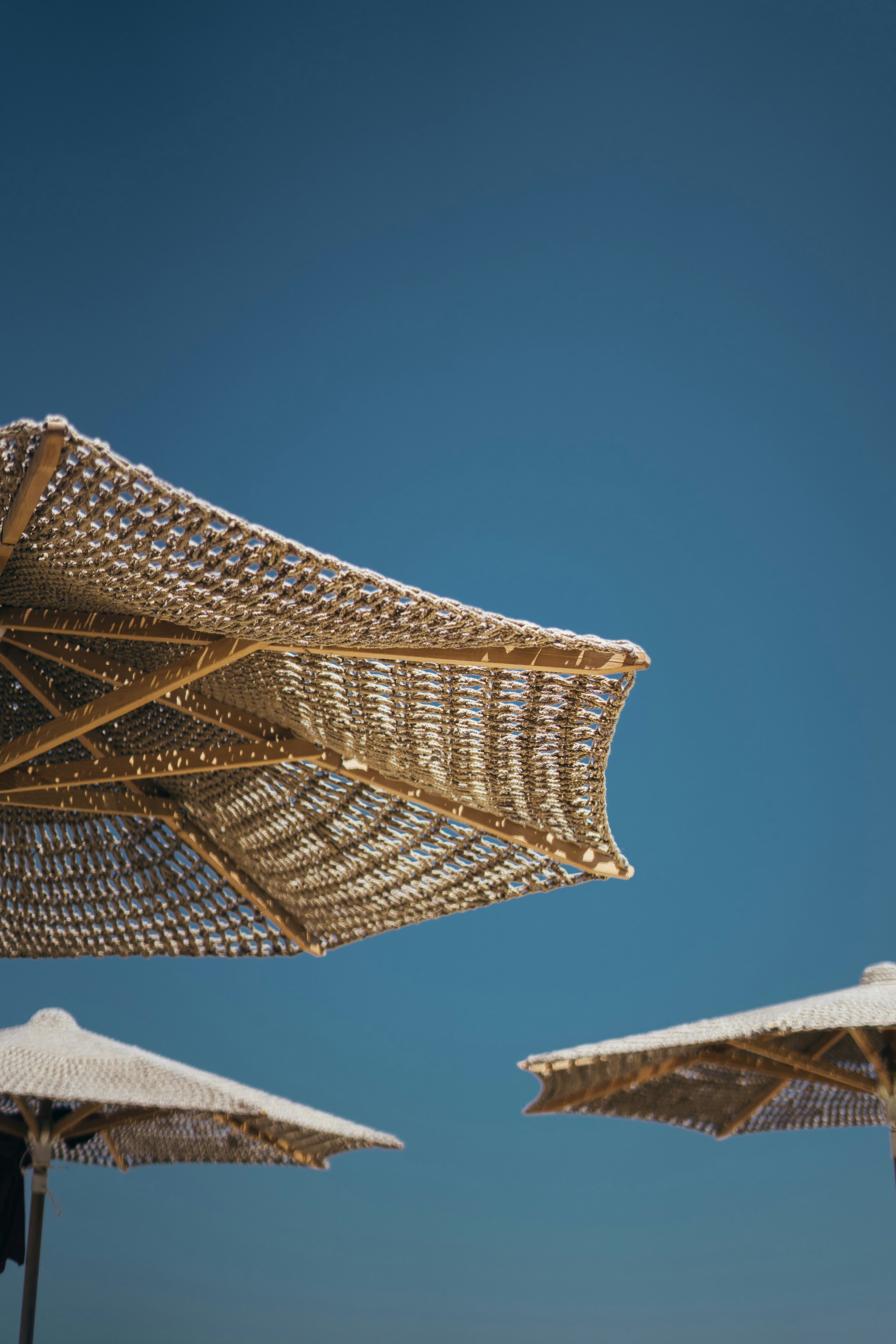 Woven beach umbrellas casting intricate shadows against a clear blue sky.