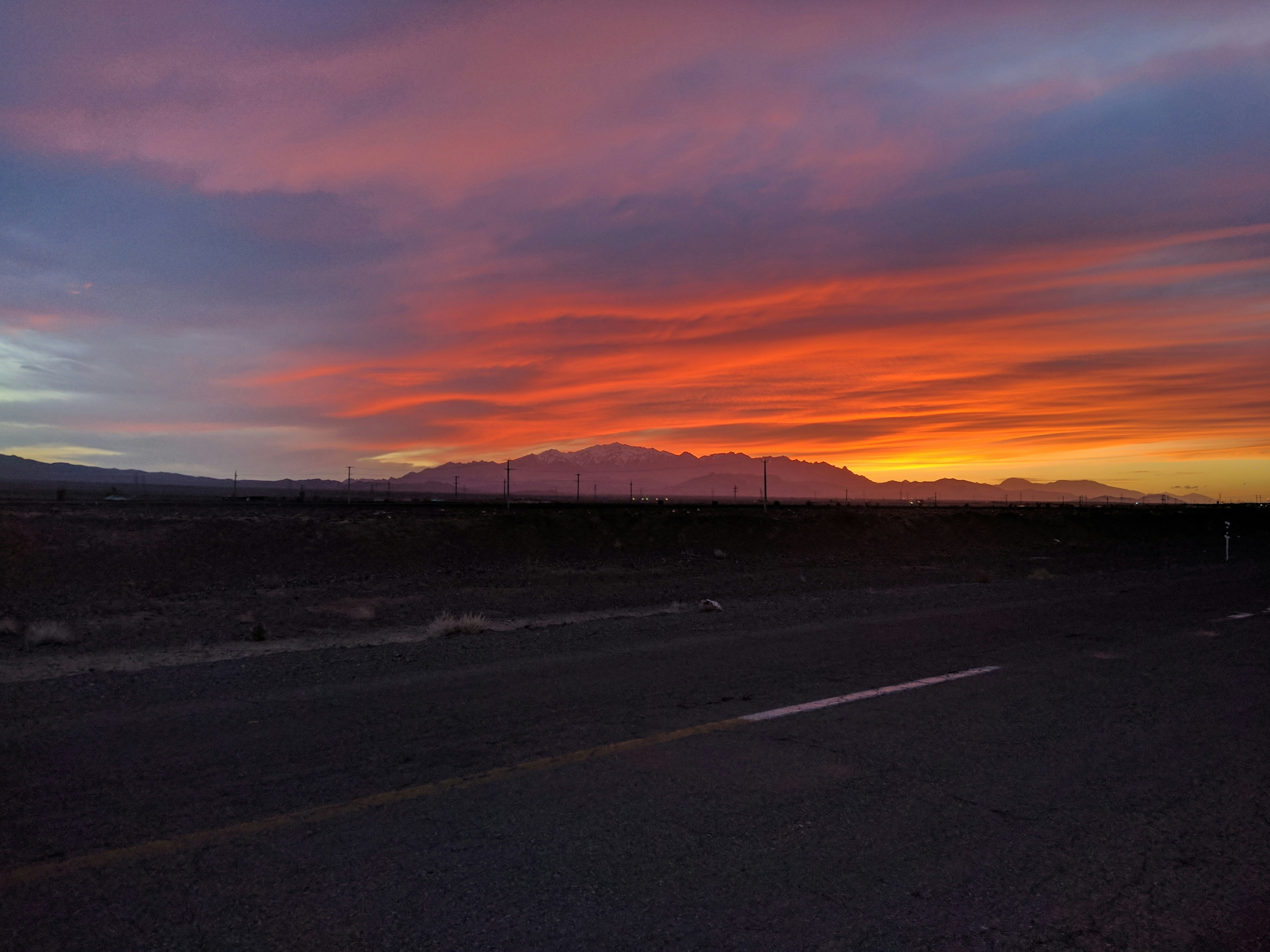 Vibrant sunset with orange and purple hues over a distant mountain range and empty road.