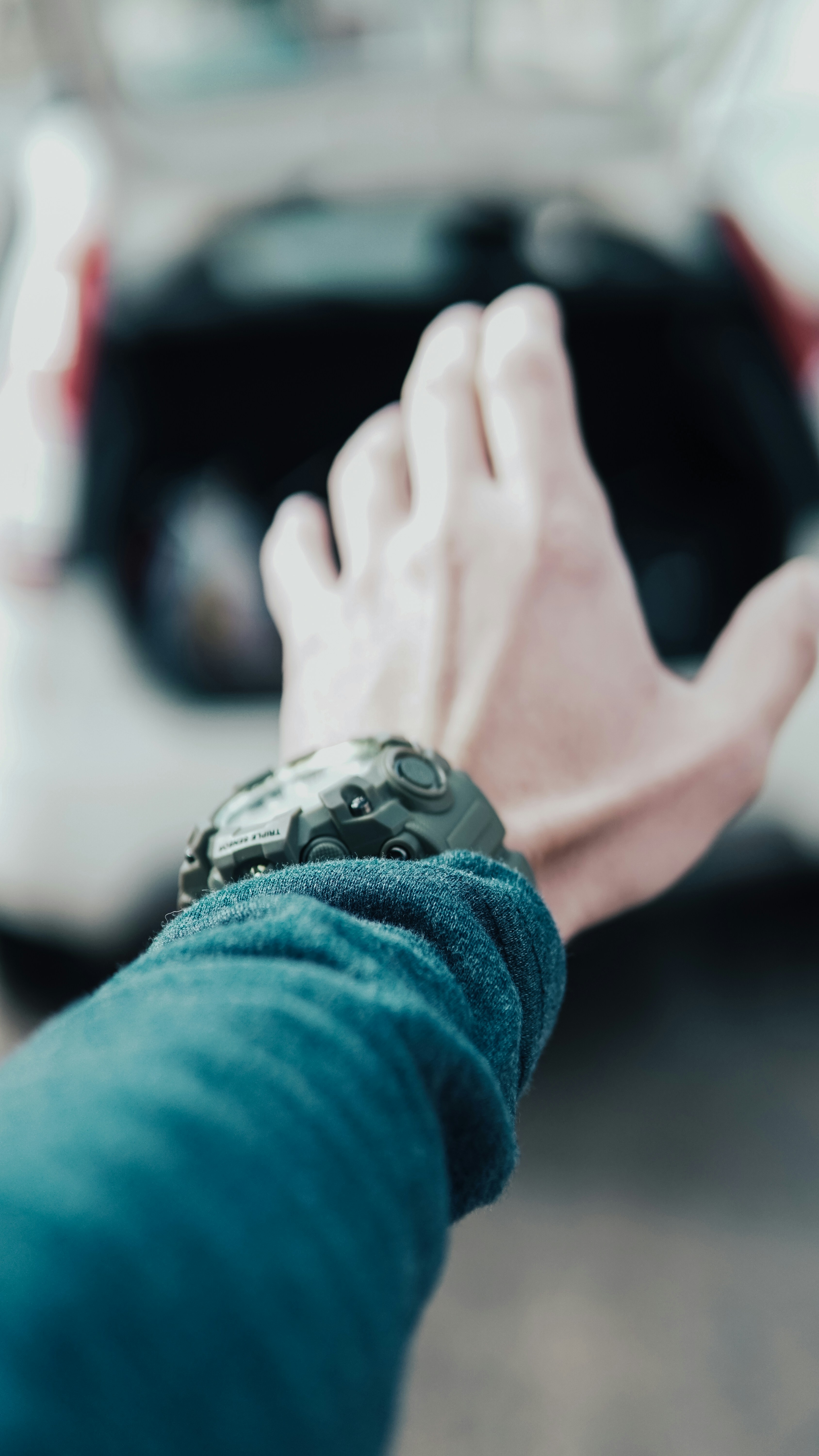 A hand extends towards an open car trunk, showcasing a watch and a textured sleeve. The background is softly blurred, emphasizing the gesture.
