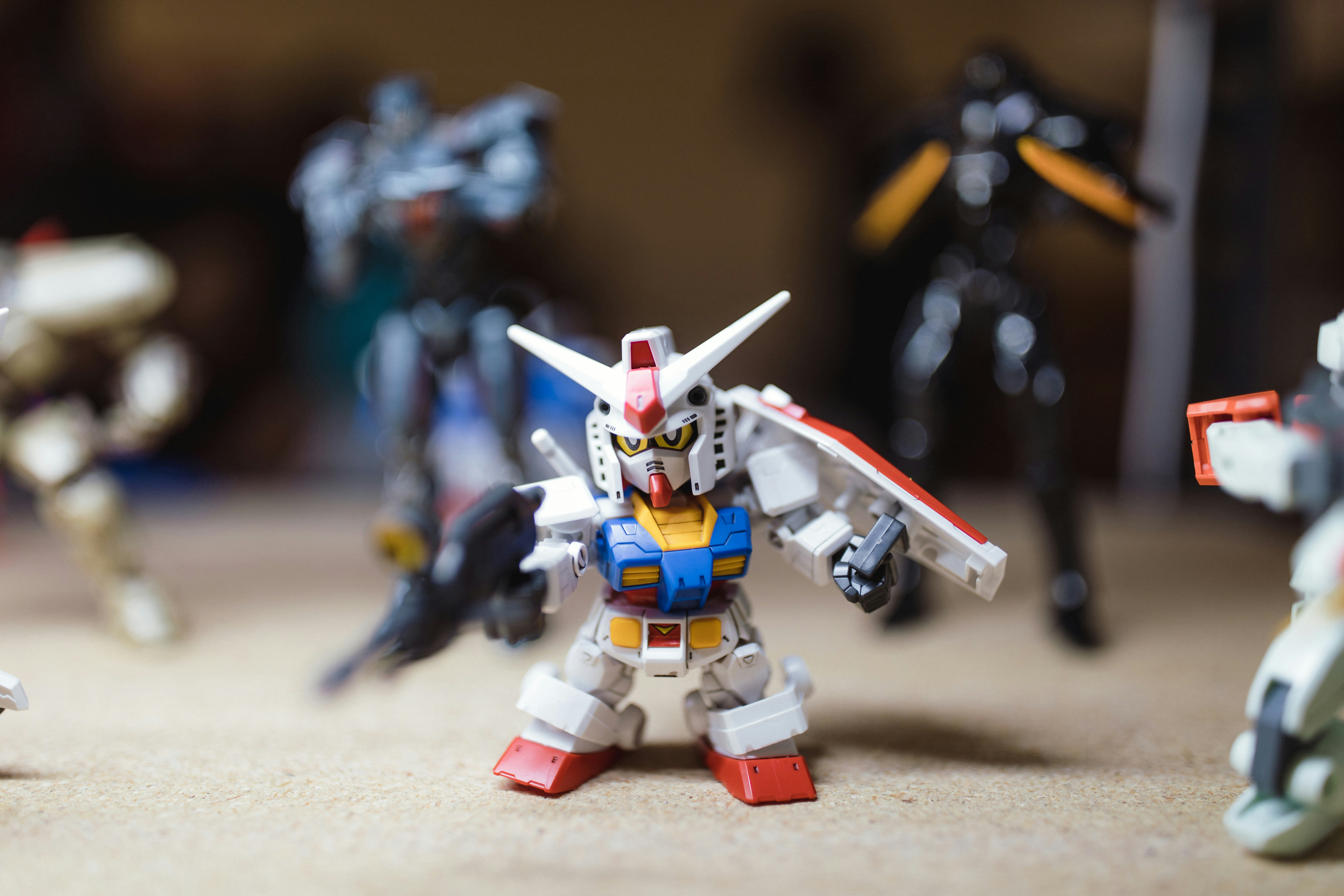 Gundam model stands prominently in the foreground with other figures blurred in the background, showcasing a dynamic display of action figures.
