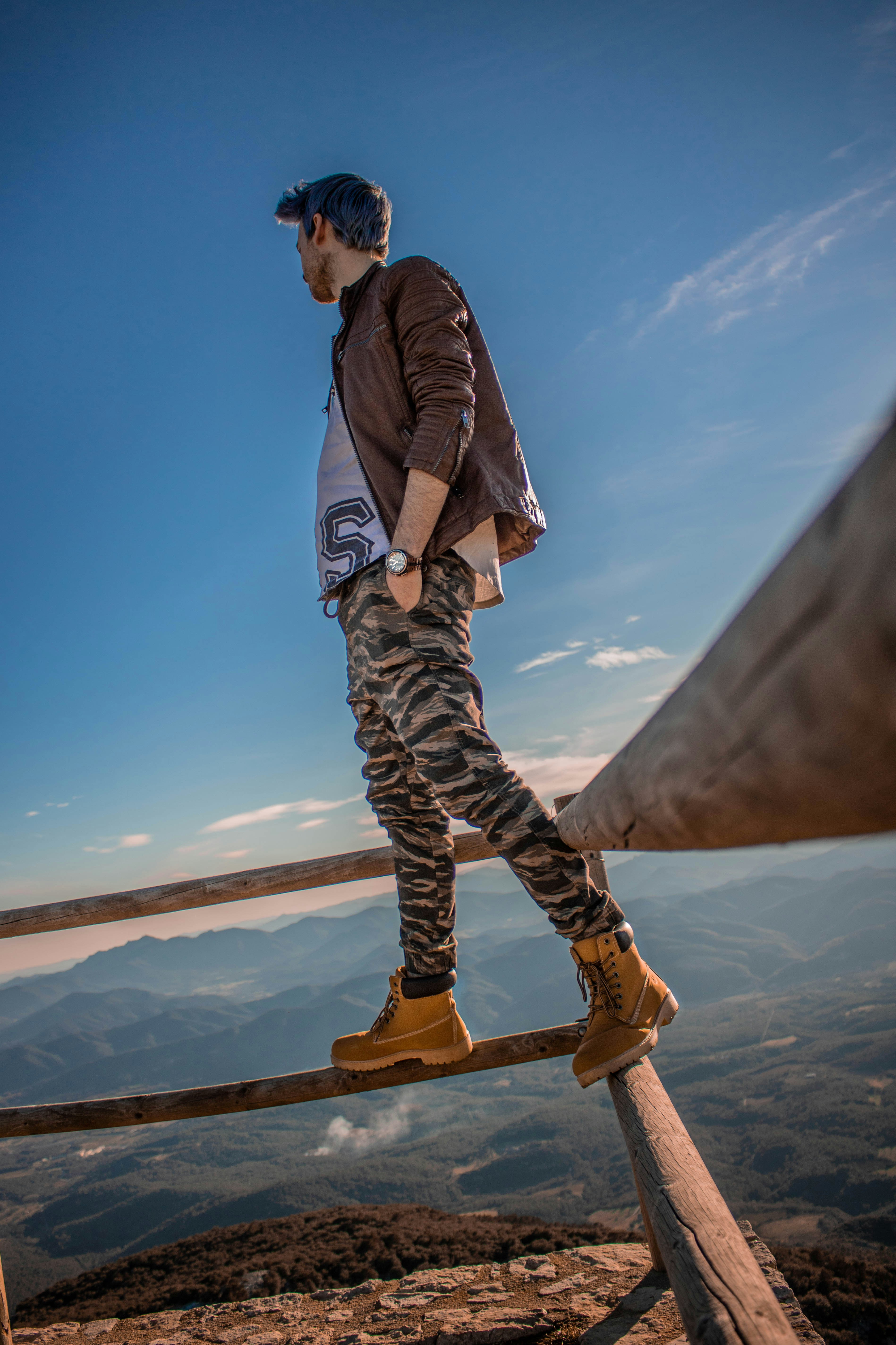 Ridge Stance: A lone climber balances along a wooden railing against a sweeping mountain panorama