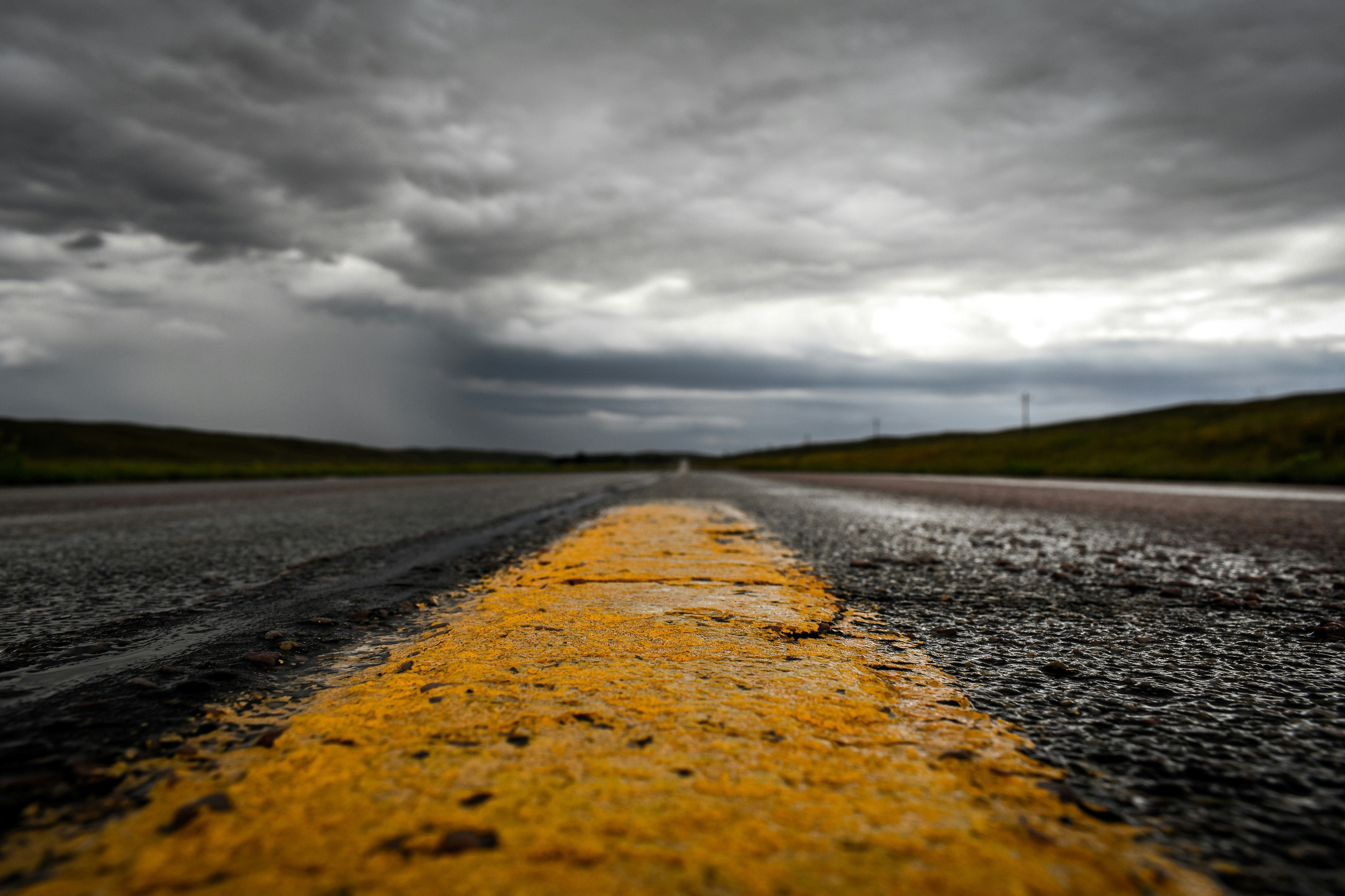 Lonely stretch of asphalt road marked by a vibrant yellow line under a dramatic sky filled with dark clouds. 