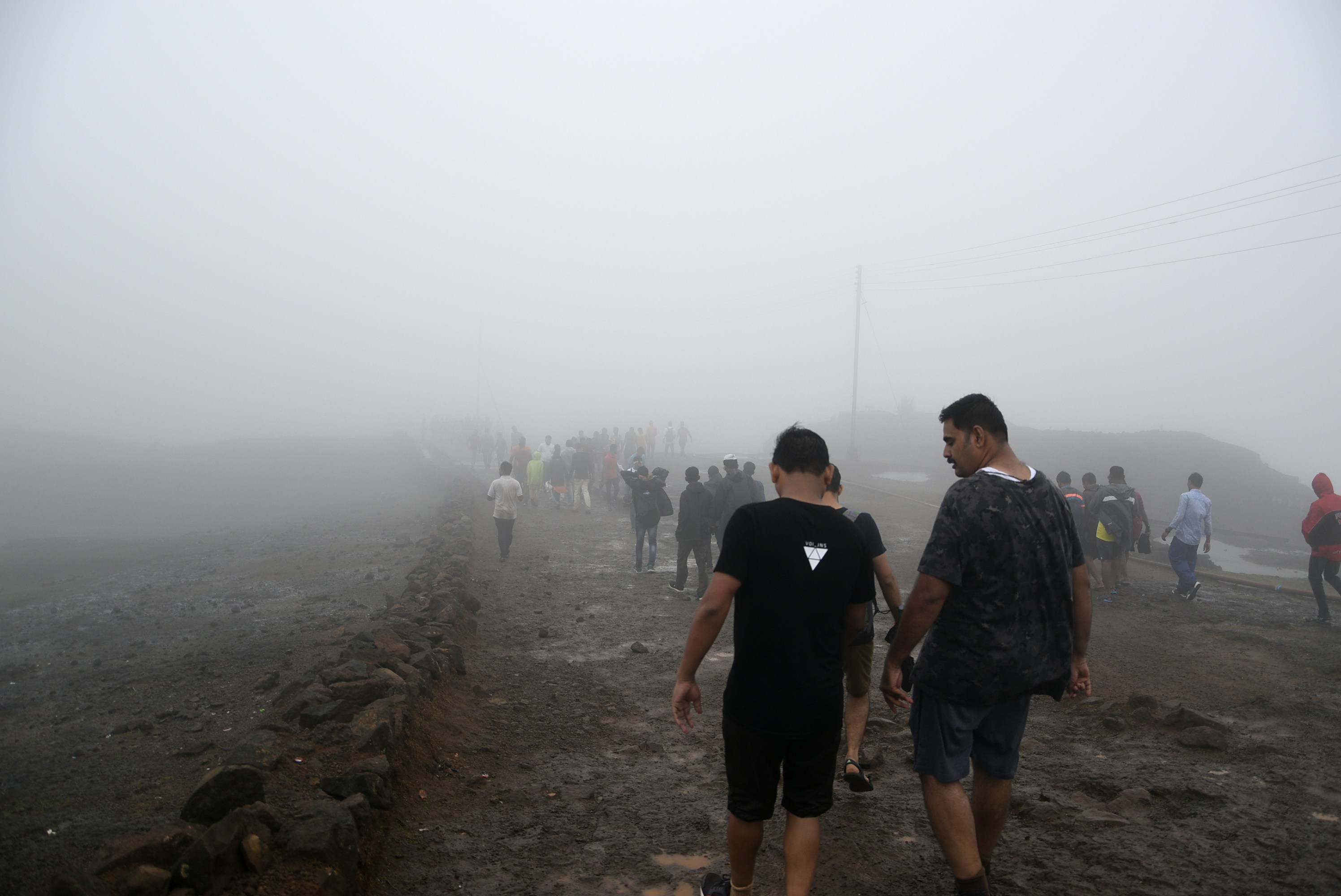 Fogbound March: Wanderers Press Forward Along a Rocky, Mist-Shrouded Path