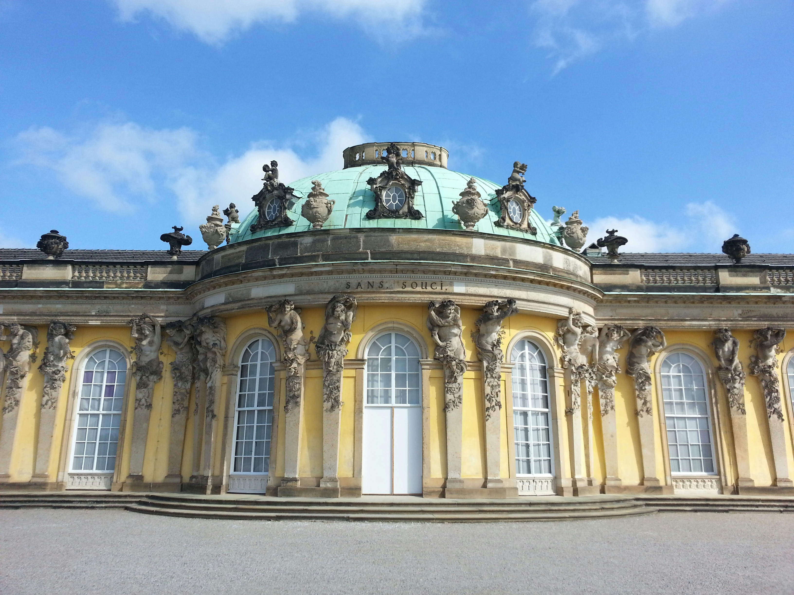 Historic yellow building with ornate sculptures and a domed roof against a bright blue sky.