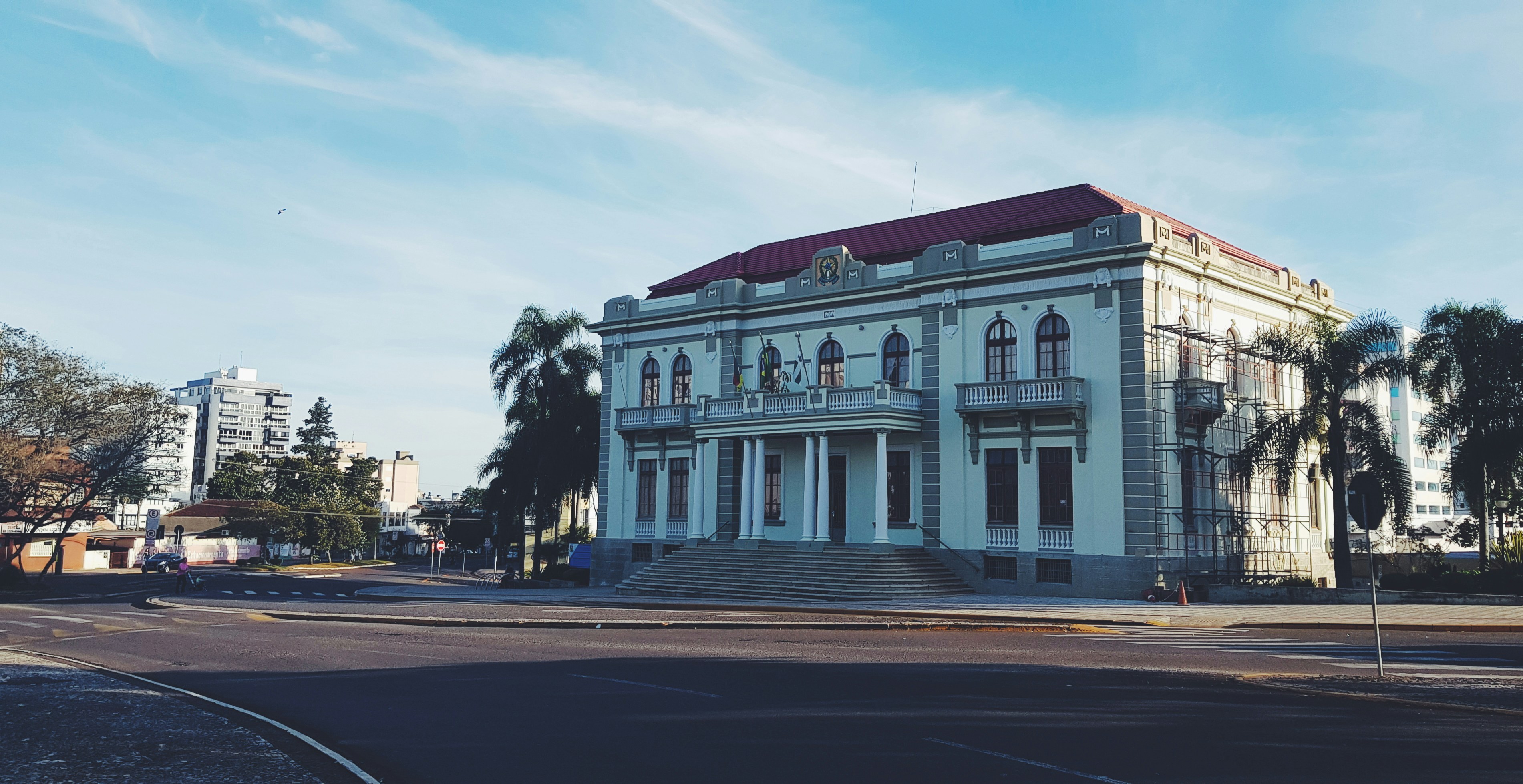 White and gray neoclassical building with a red roof under a clear blue sky.