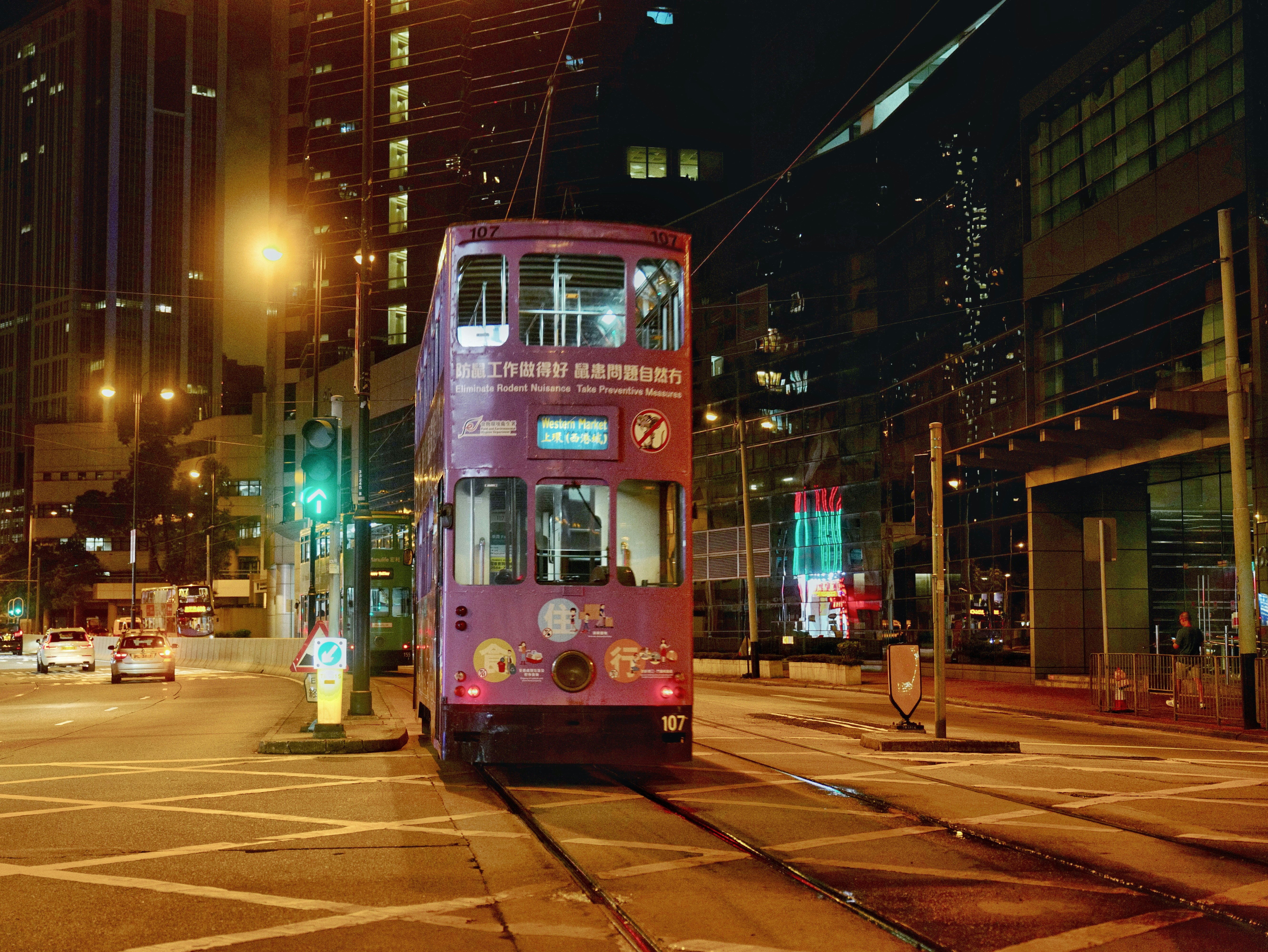 A vintage tram illuminated by city lights, showcasing vibrant advertisements against a bustling urban backdrop at night.