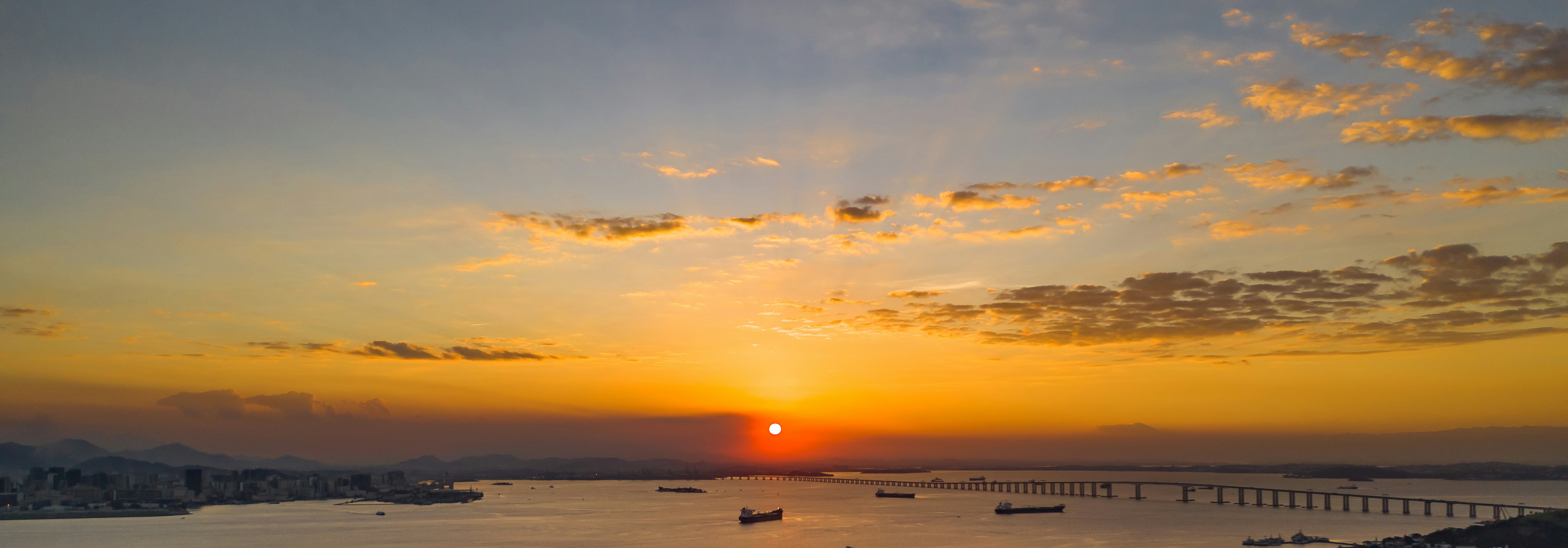 Sunset casts a warm glow over a dock with scattered clouds and calm waters.