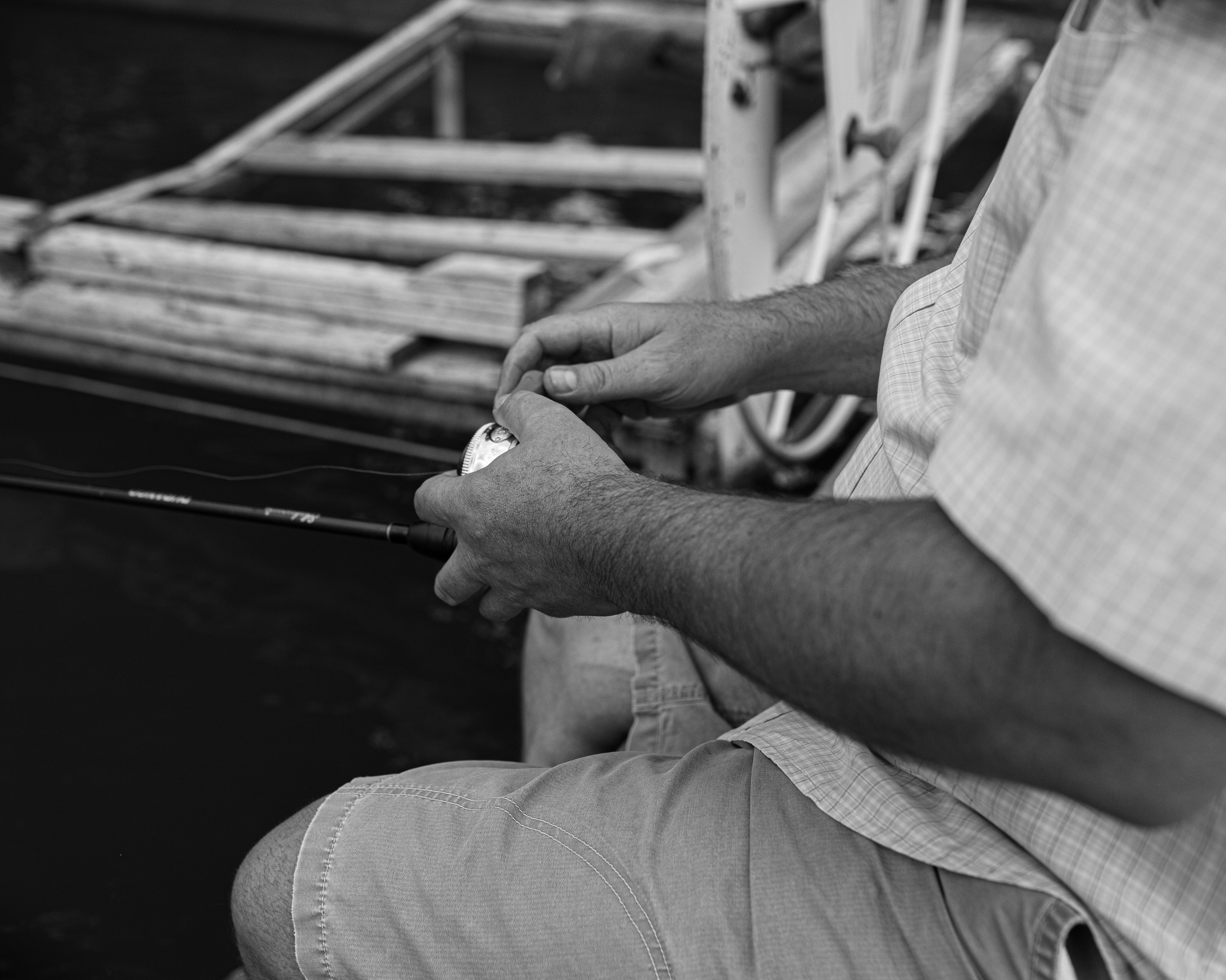 Close-up of a man's hands delicately handling fishing gear while seated by the water, conveying a sense of tranquility and focus.