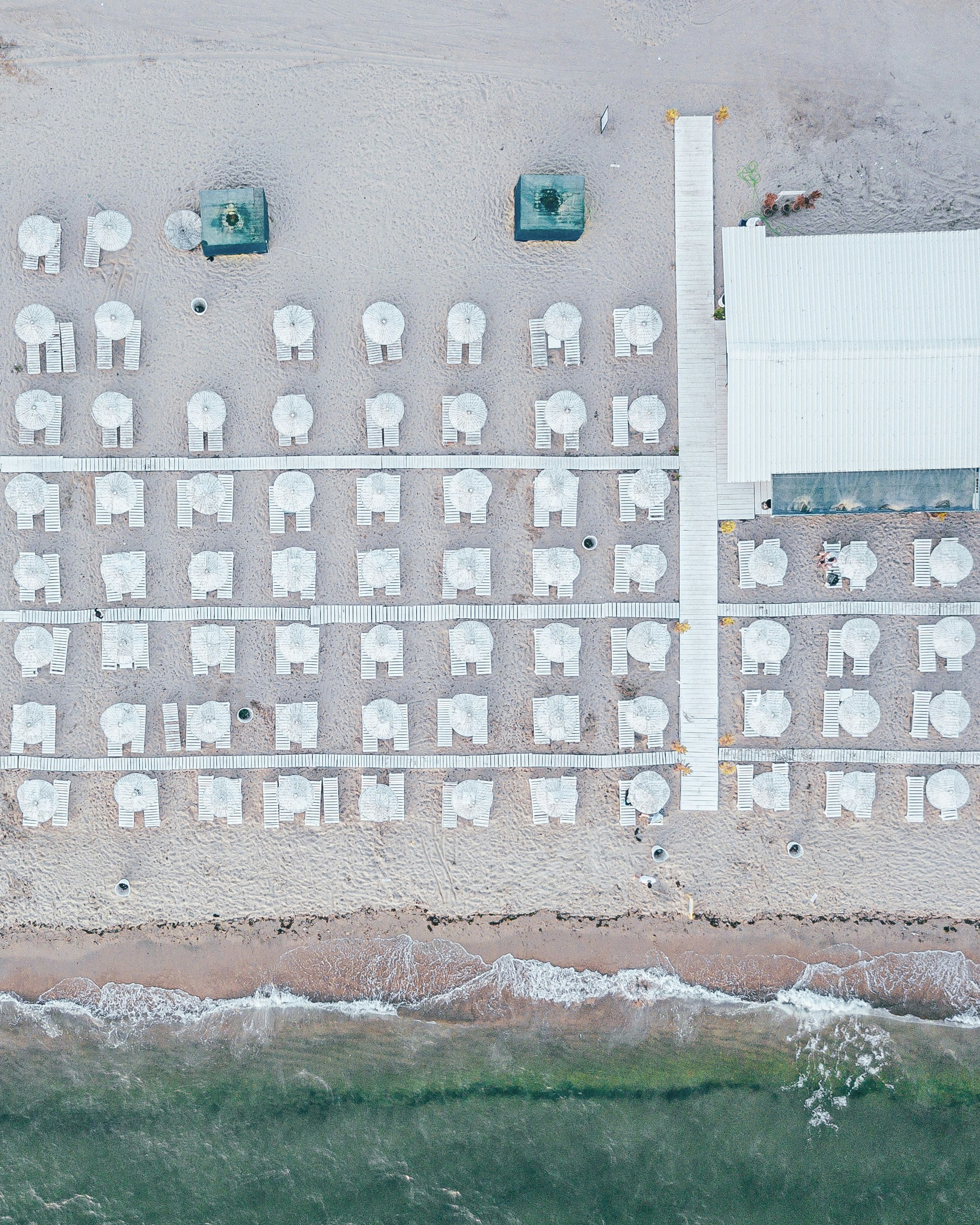 Aerial view of a meticulously arranged beach with numerous sunbeds and umbrellas, leading to the shoreline. The scene captures the essence of relaxation by the sea.