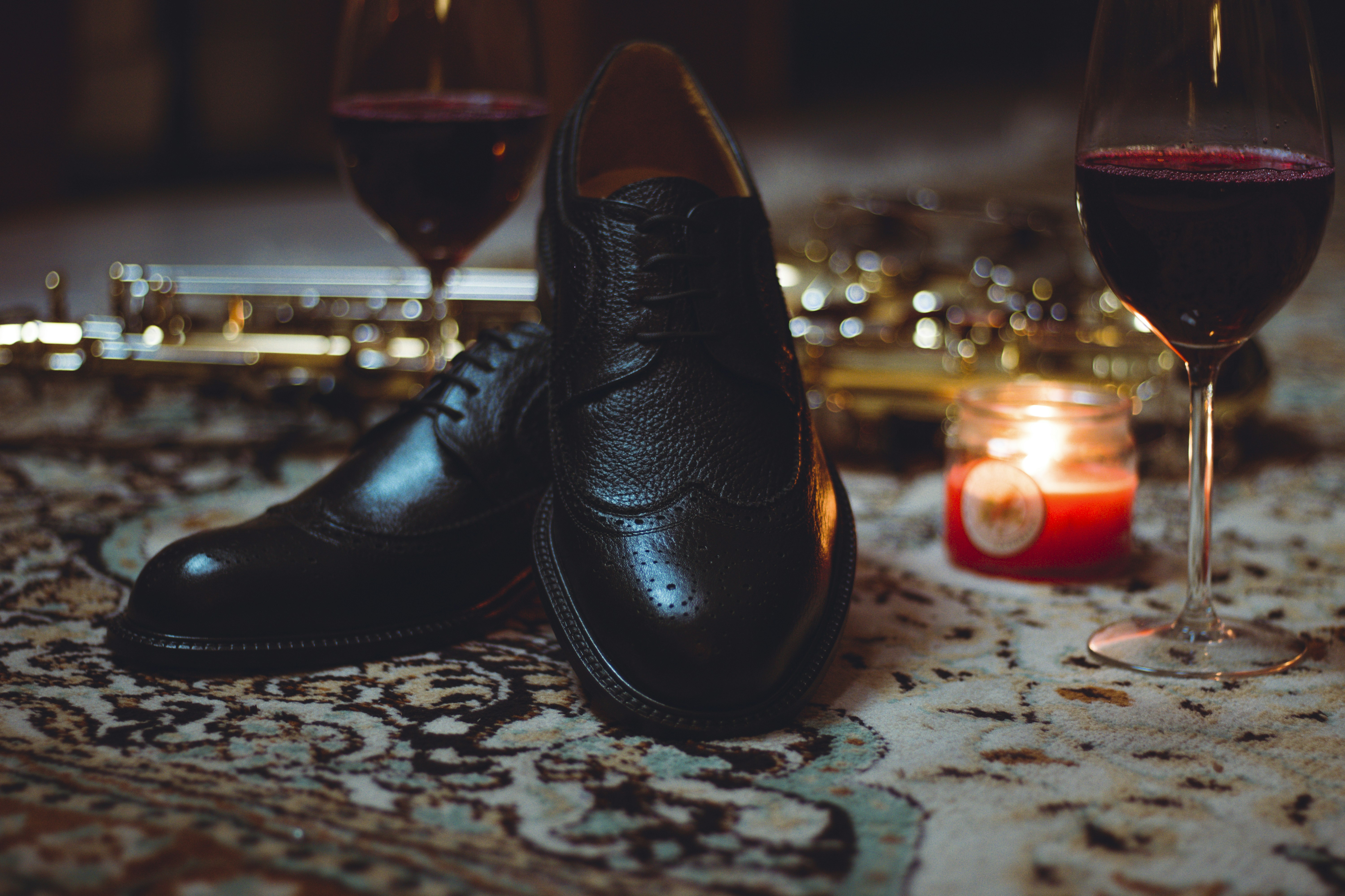 Candlelit Quiet: Black Oxfords Rest on a Patterned Table Under Gentle Glow