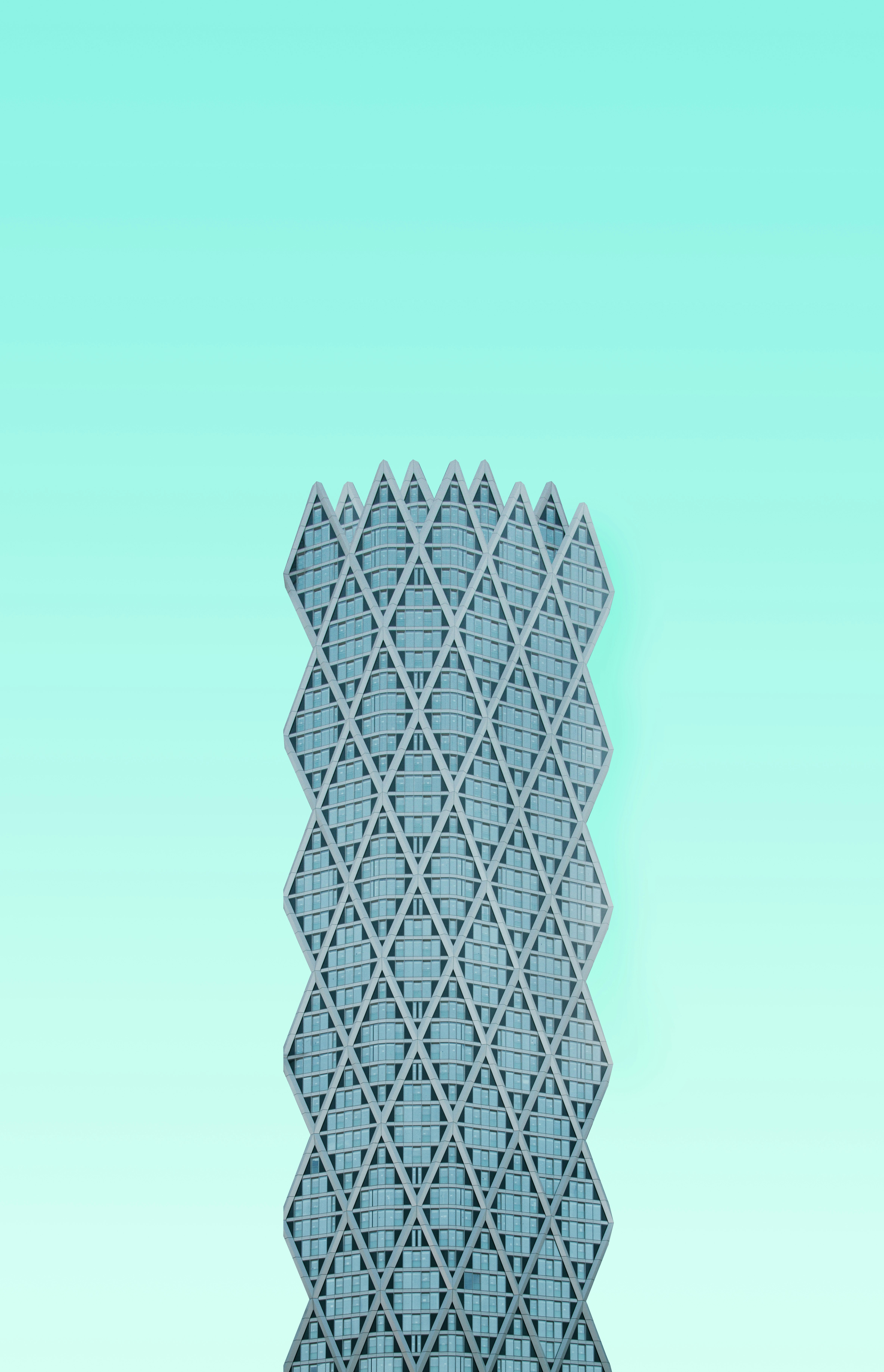 A striking modern building with a geometric facade, showcasing intricate glass patterns against a soft turquoise backdrop.