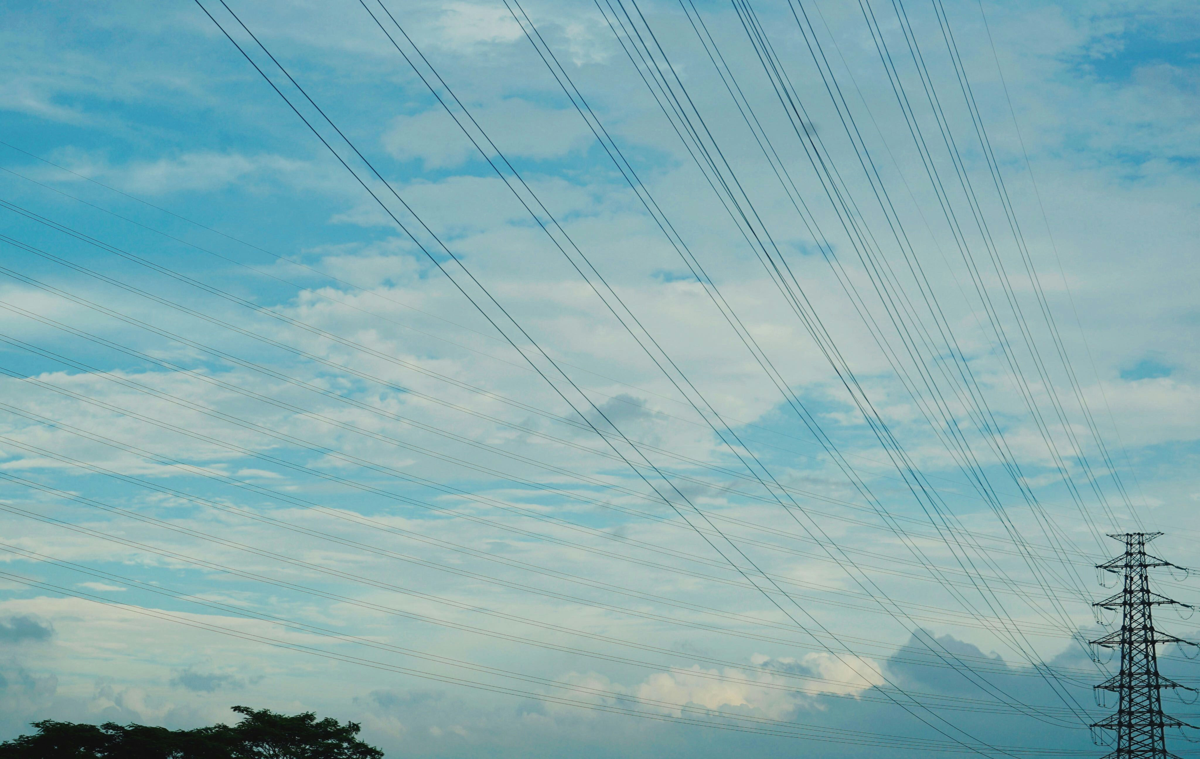 Electricity pylons rise against a backdrop of textured clouds and a vast blue sky.