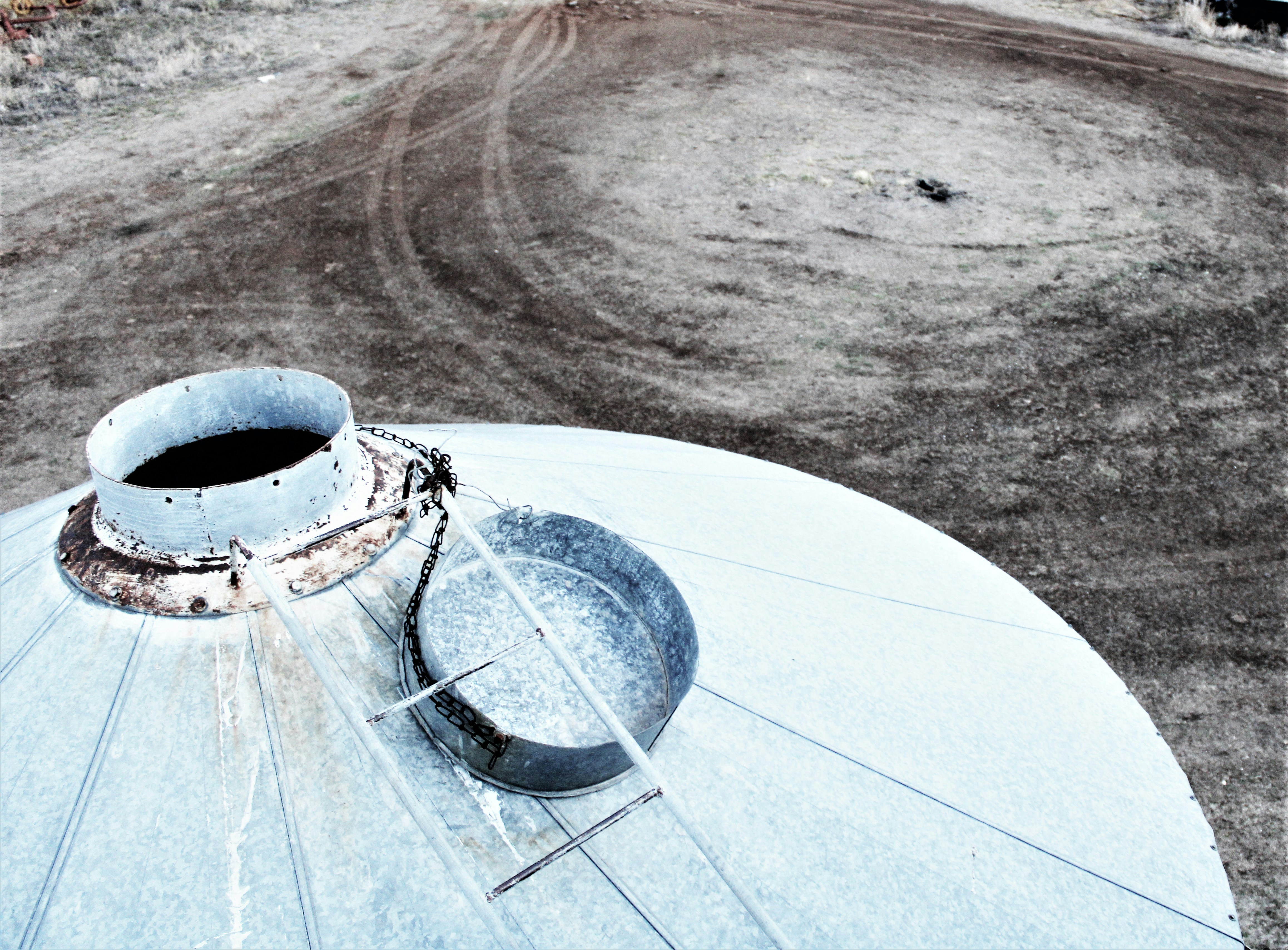 Top of the Tank: Weathered Vent Cap Framed Against Bare Ground