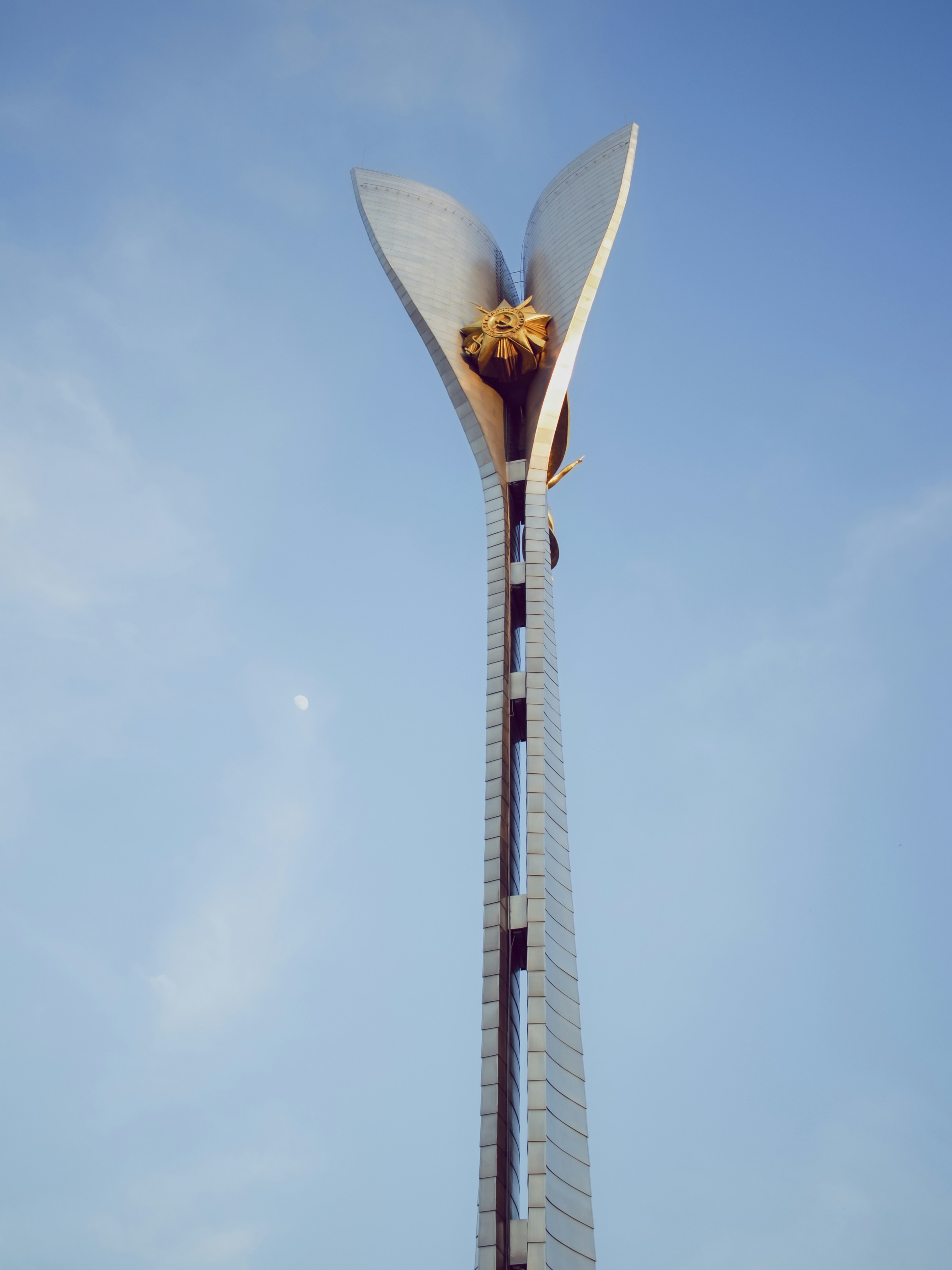 Towering monument with a golden emblem at its peak, reaching towards a clear blue sky.