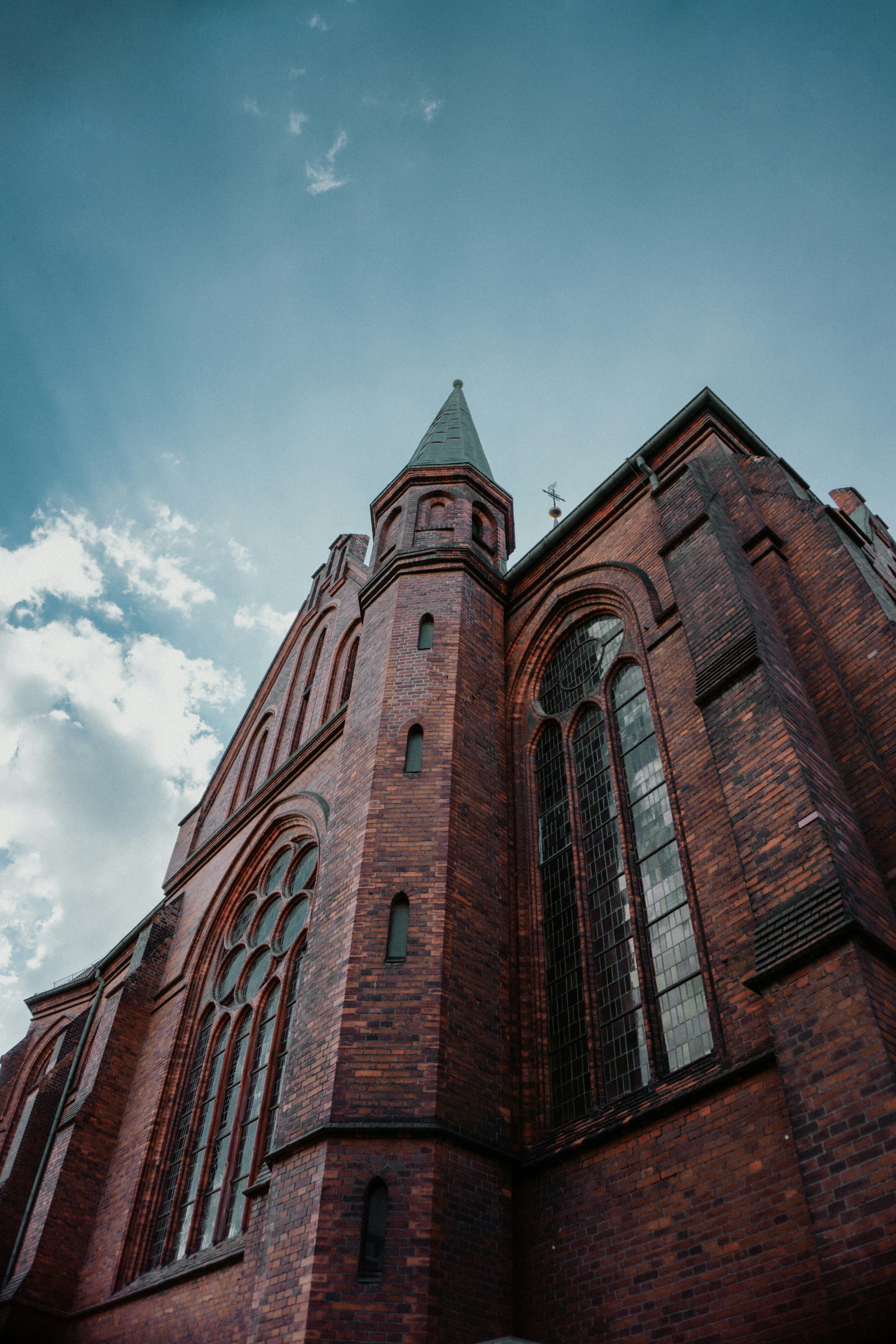 Imposing brick church structure with a tall spire, showcasing intricate architectural details against a cloudy sky.