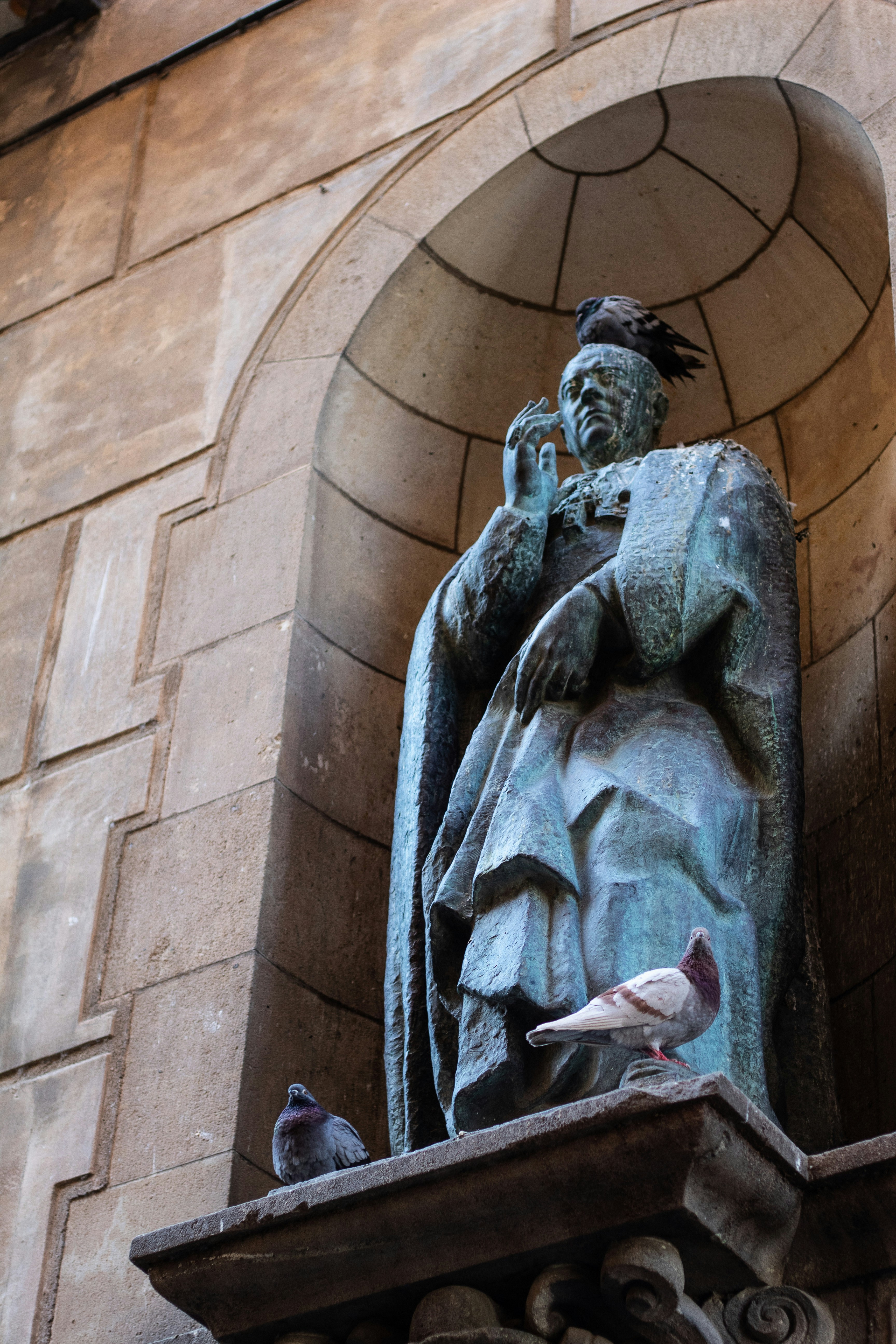 Bronze statue of a historical figure adorned with a pigeon on its head, flanked by two other pigeons on a stone ledge.