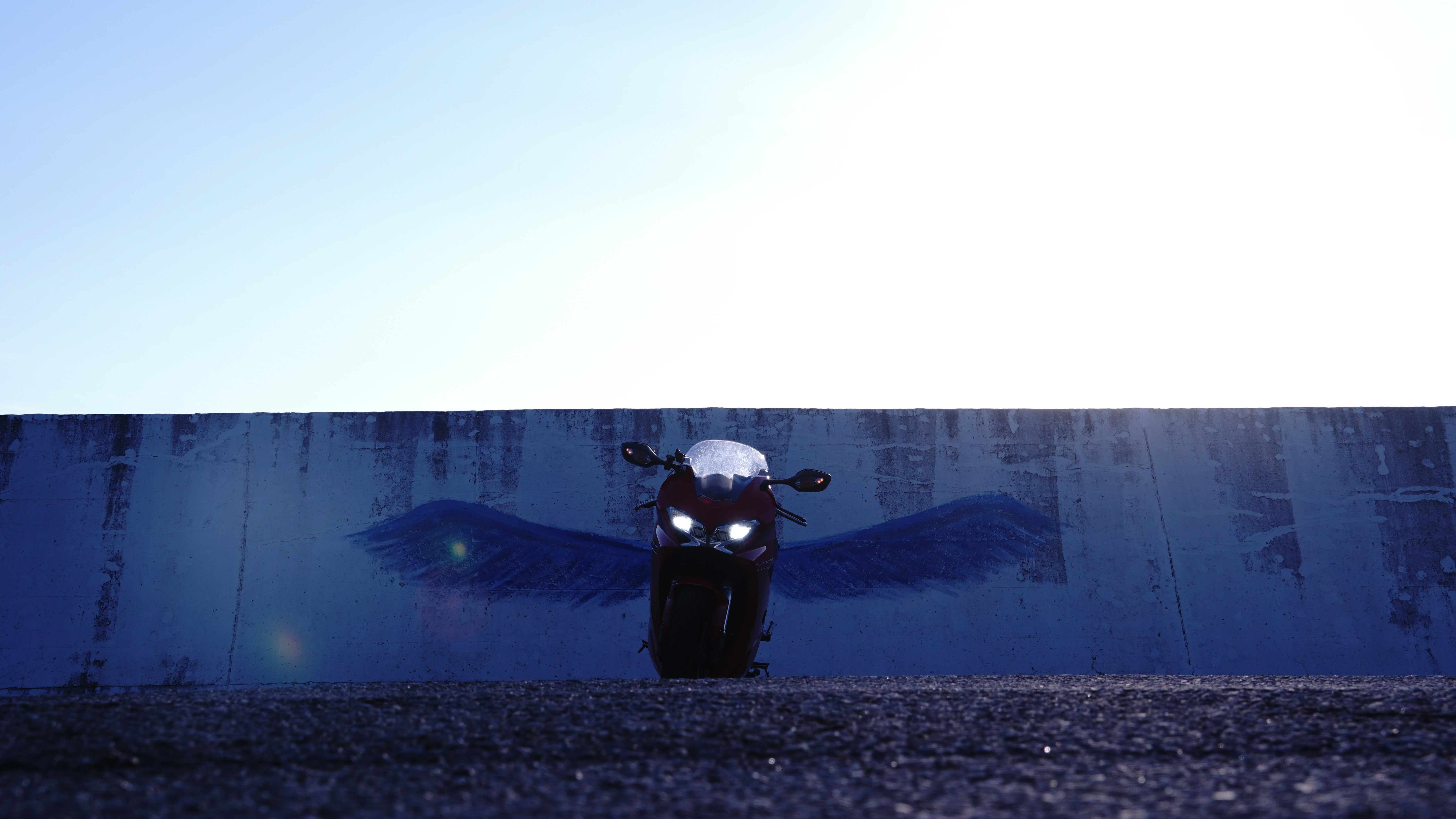 Motorcycle positioned against a wall with shadow resembling wings in bright sunlight.